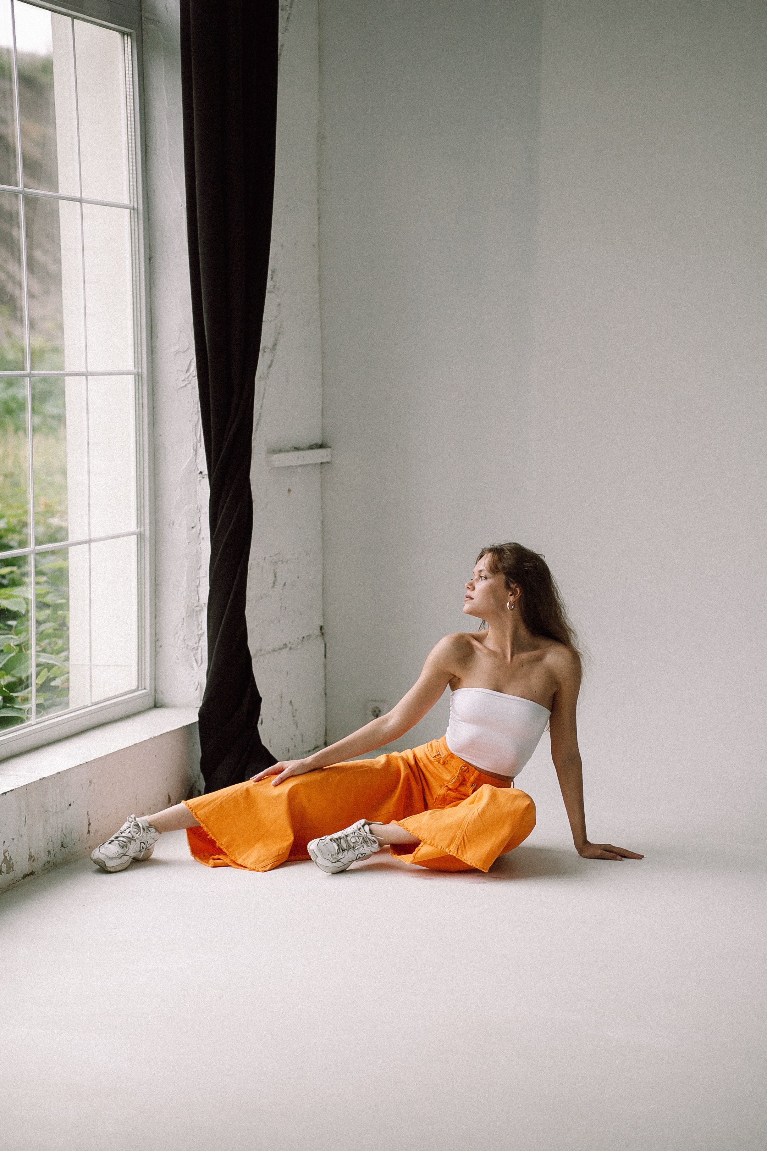 A Female Model Sitting on Concrete Floor and Looking Through a Window ...