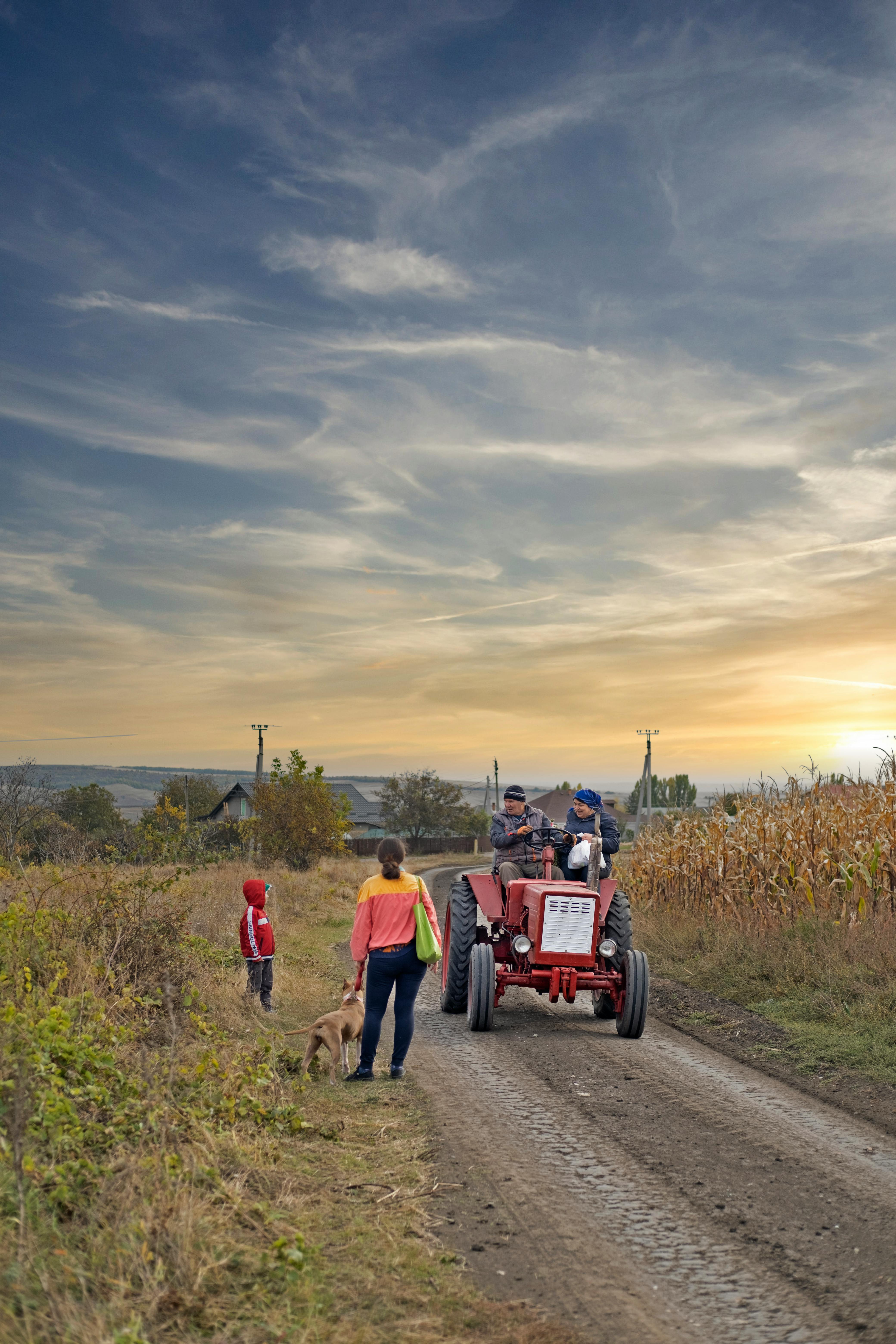 Two Men Riding Red Tractor on Rural Road During Sunset · Free Stock Photo