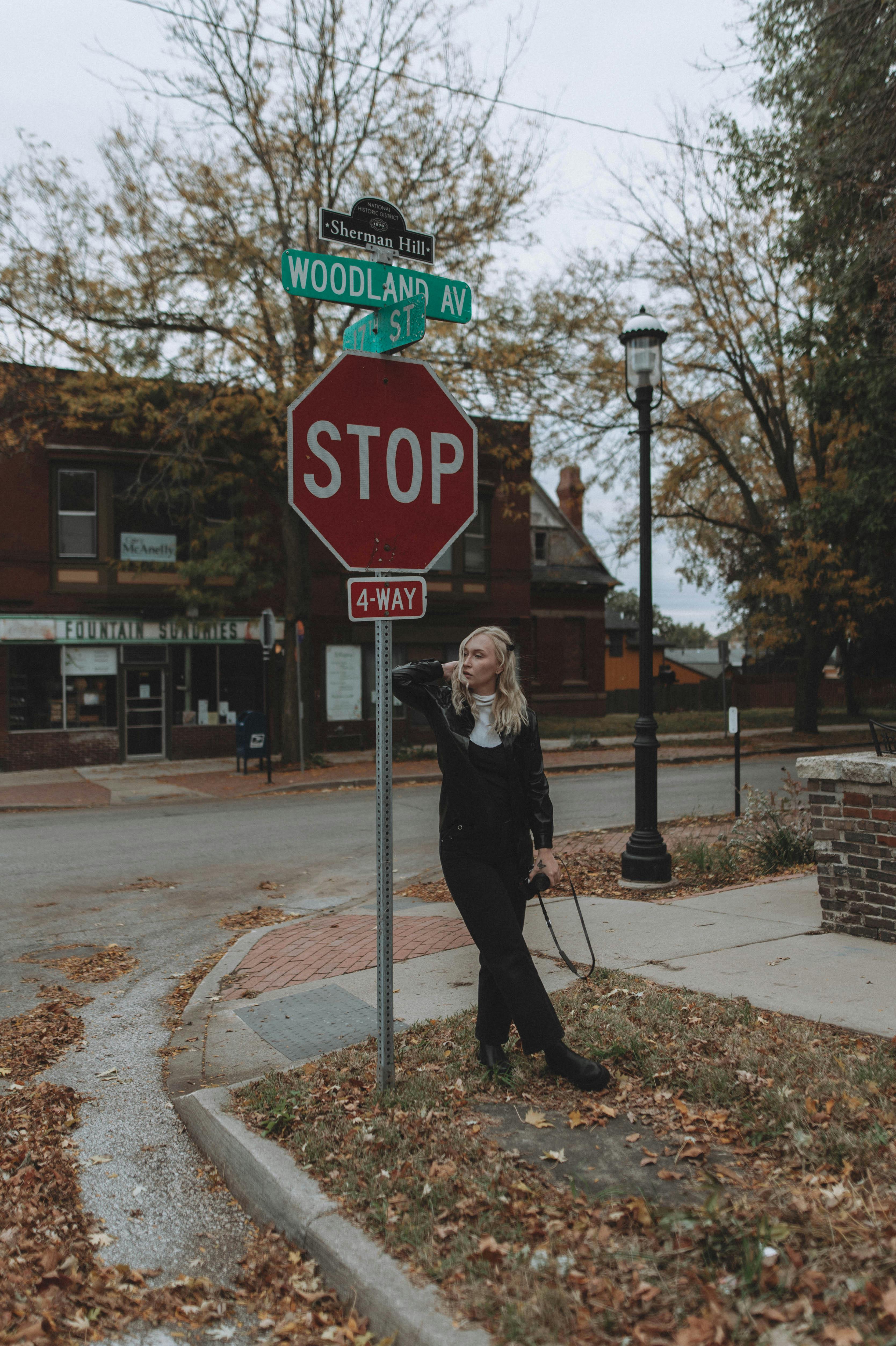 Blond Woman in Black Clothing Leaning Against Stop Sign · Free Stock Photo
