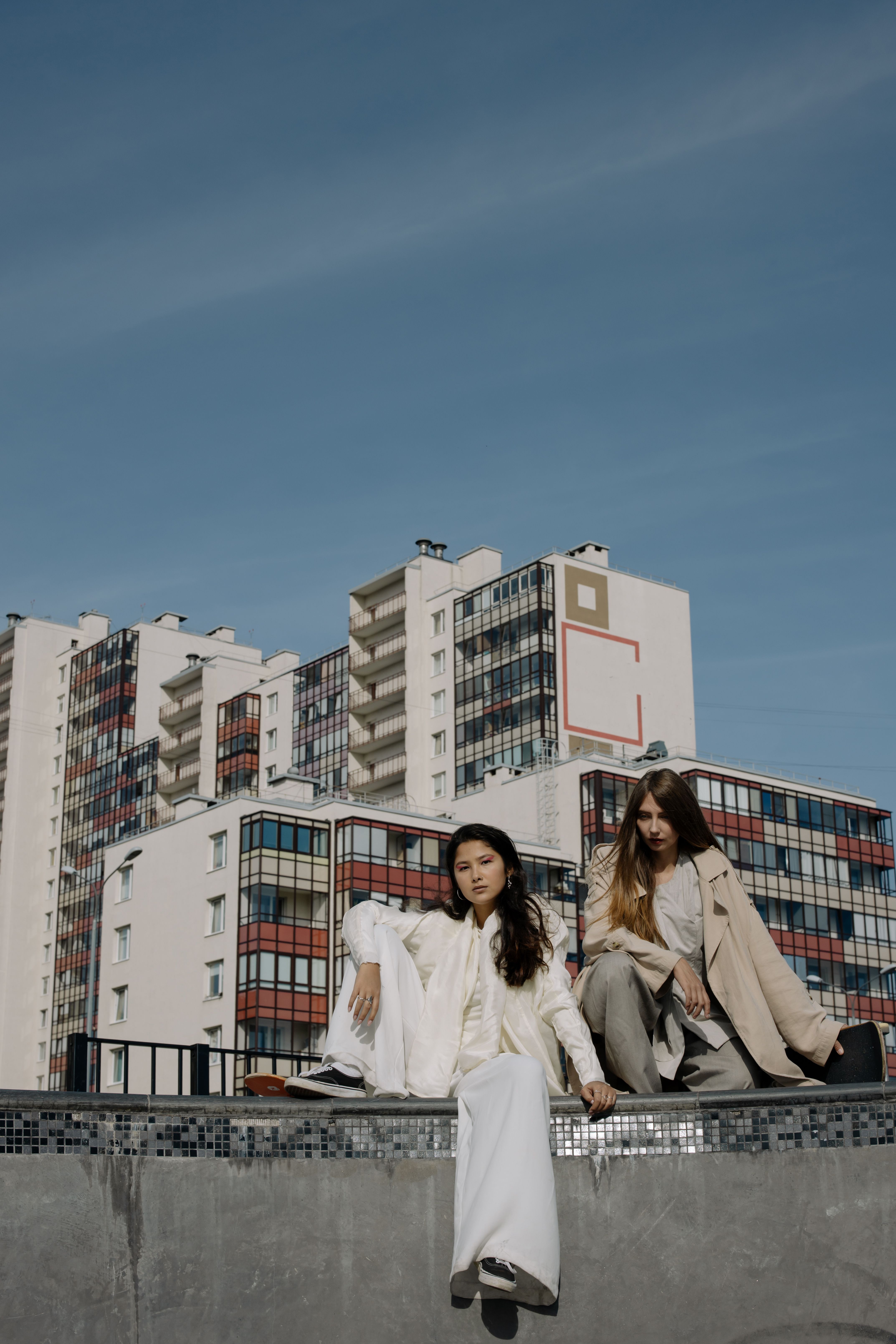 Women Sitting on a Concrete Fence Near Tall Buildings · Free Stock Photo