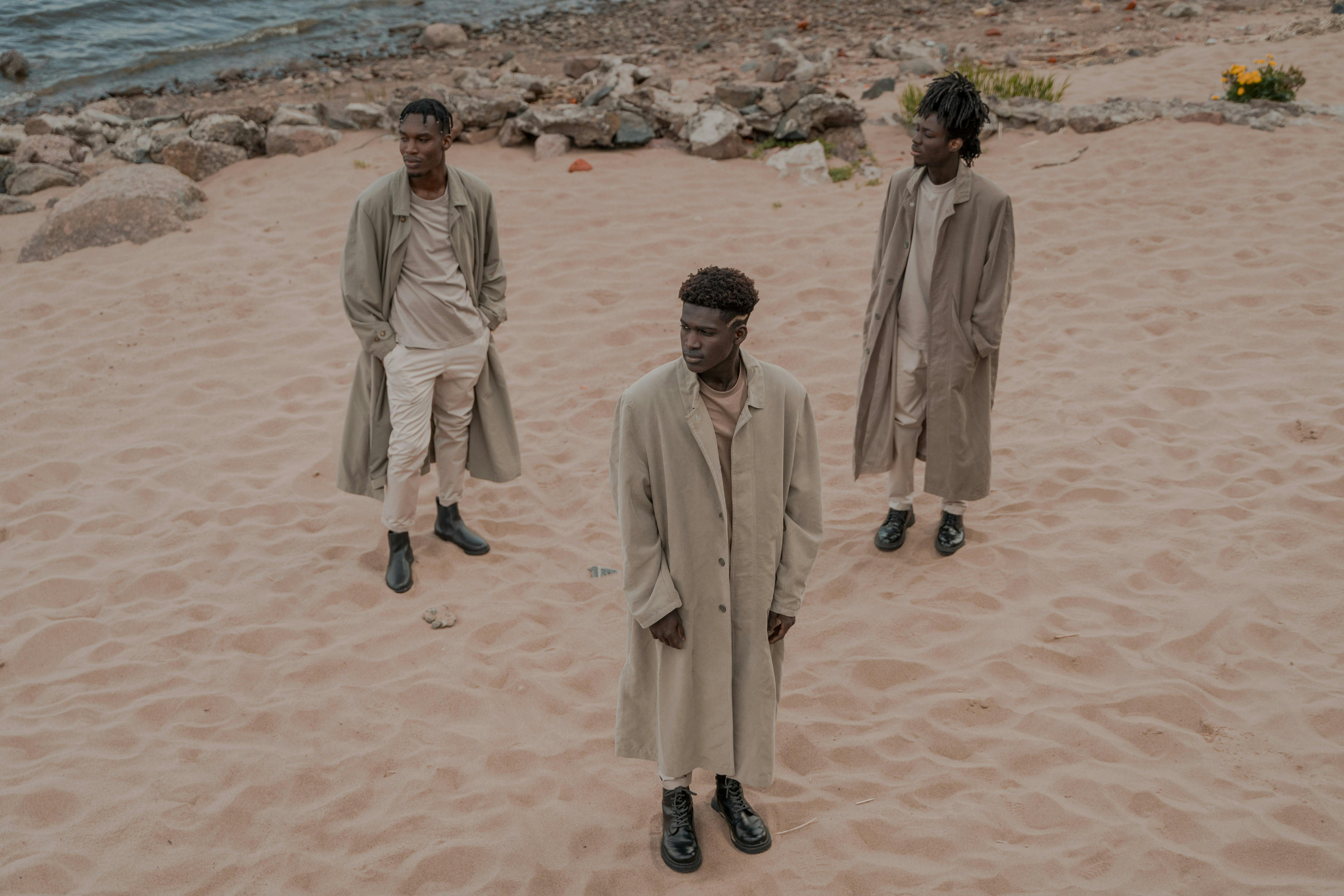 Three Men in Neutral Colored Clothing Standing on Sand · Free Stock Photo