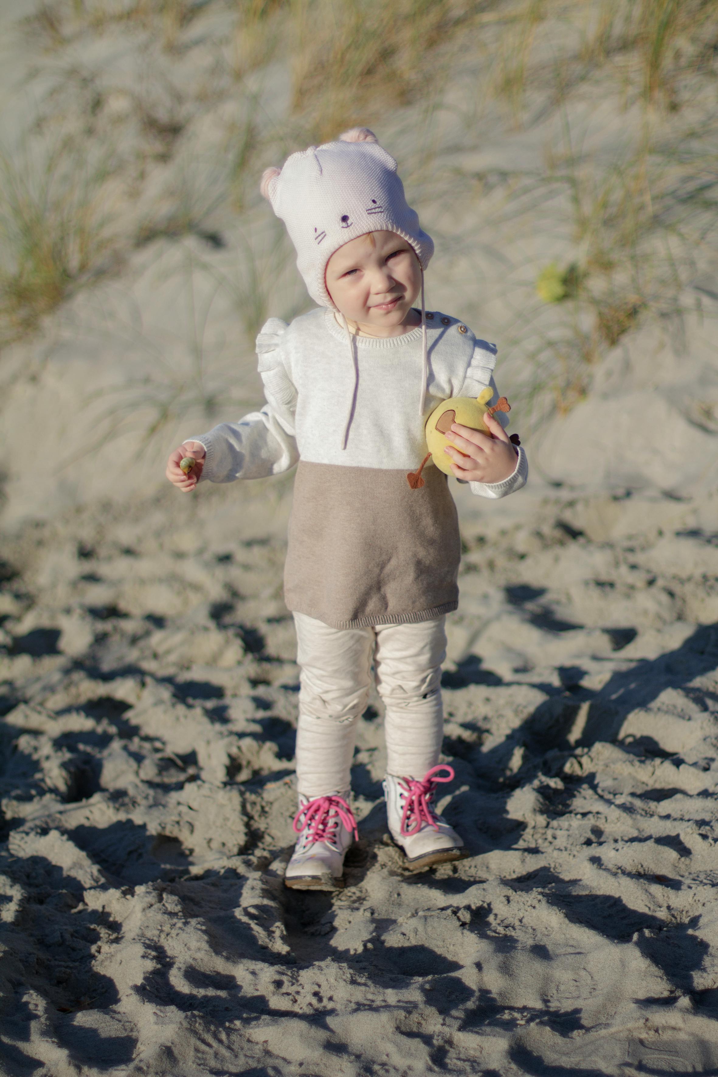 Child with Bonnet Standing on Gray Sand · Free Stock Photo