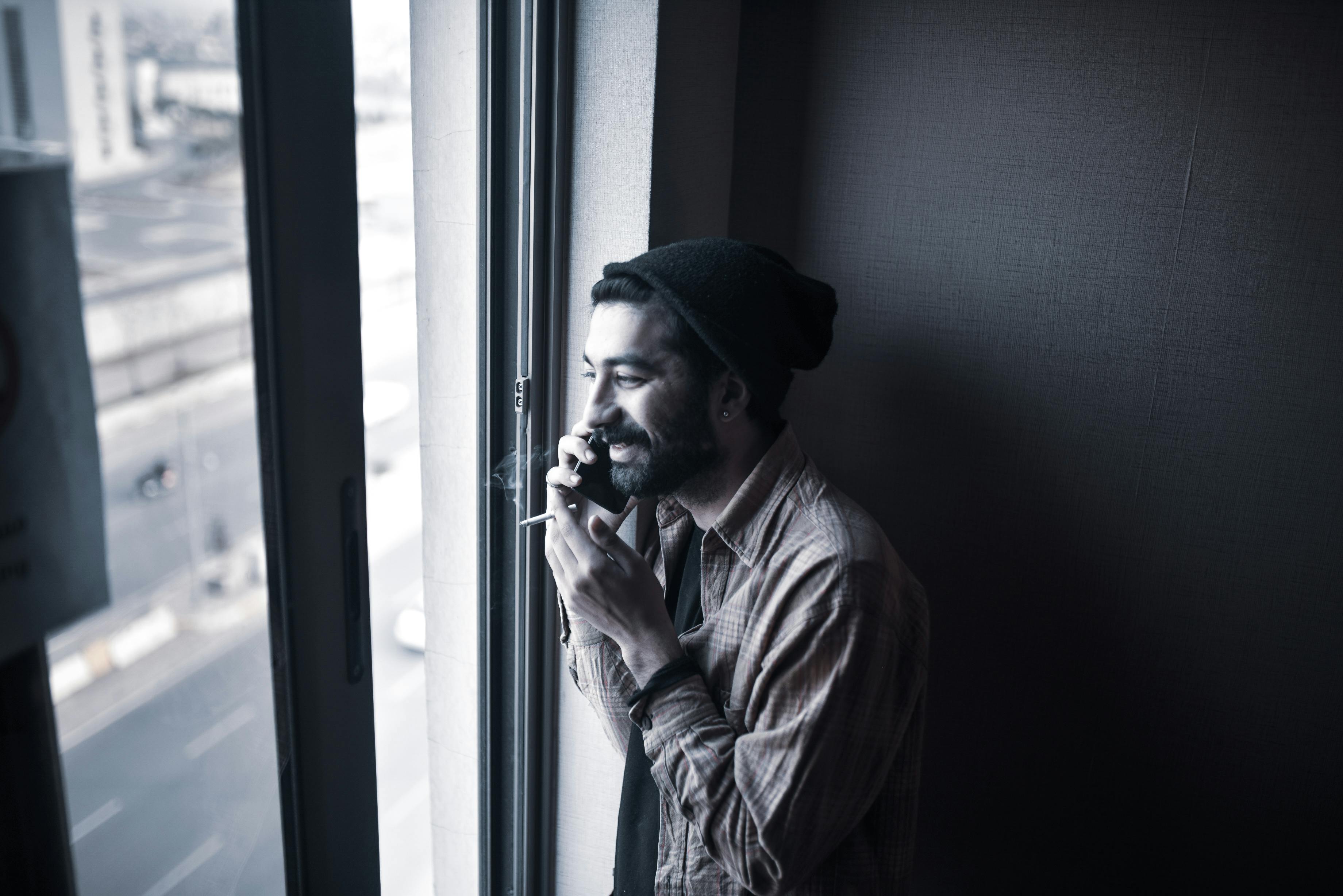 Grayscale Photo of a Man Beside Window Smoking Cigarette While Talking ...
