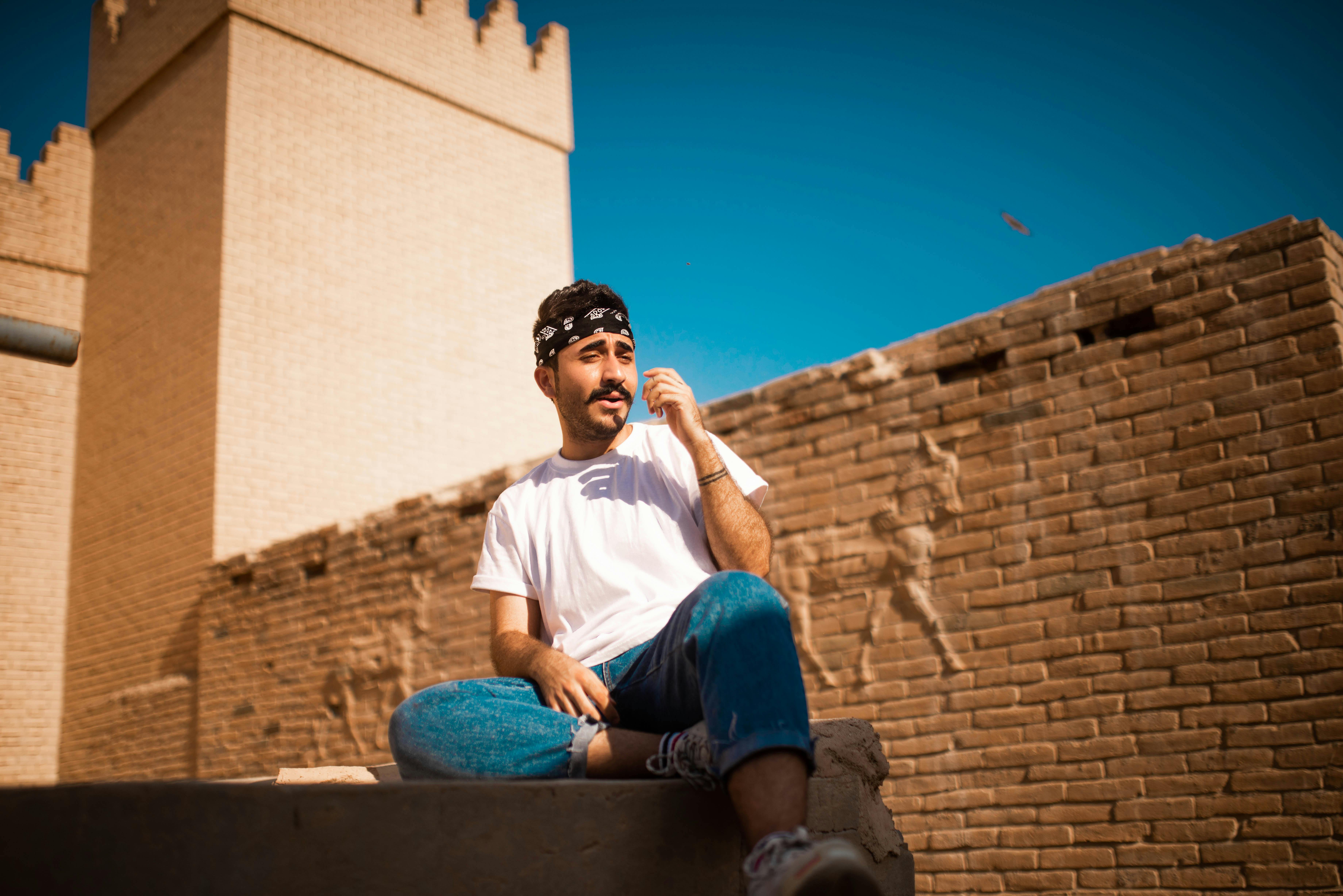 A Man Wearing a White Shirt and Denim Pants Crouching · Free Stock Photo