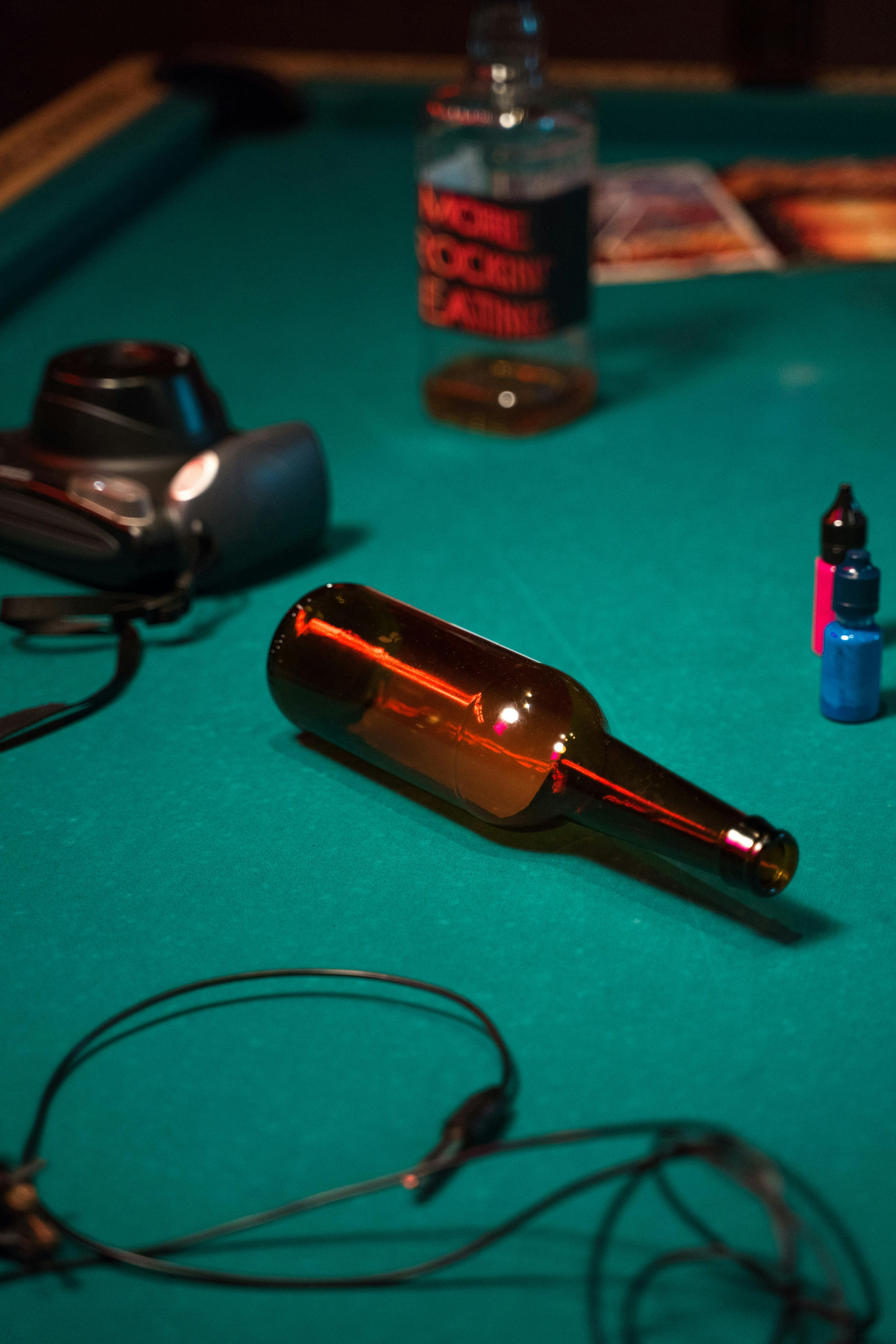 Beer Bottle Beside Black Camera and Charging Cable on Billiard Table ...
