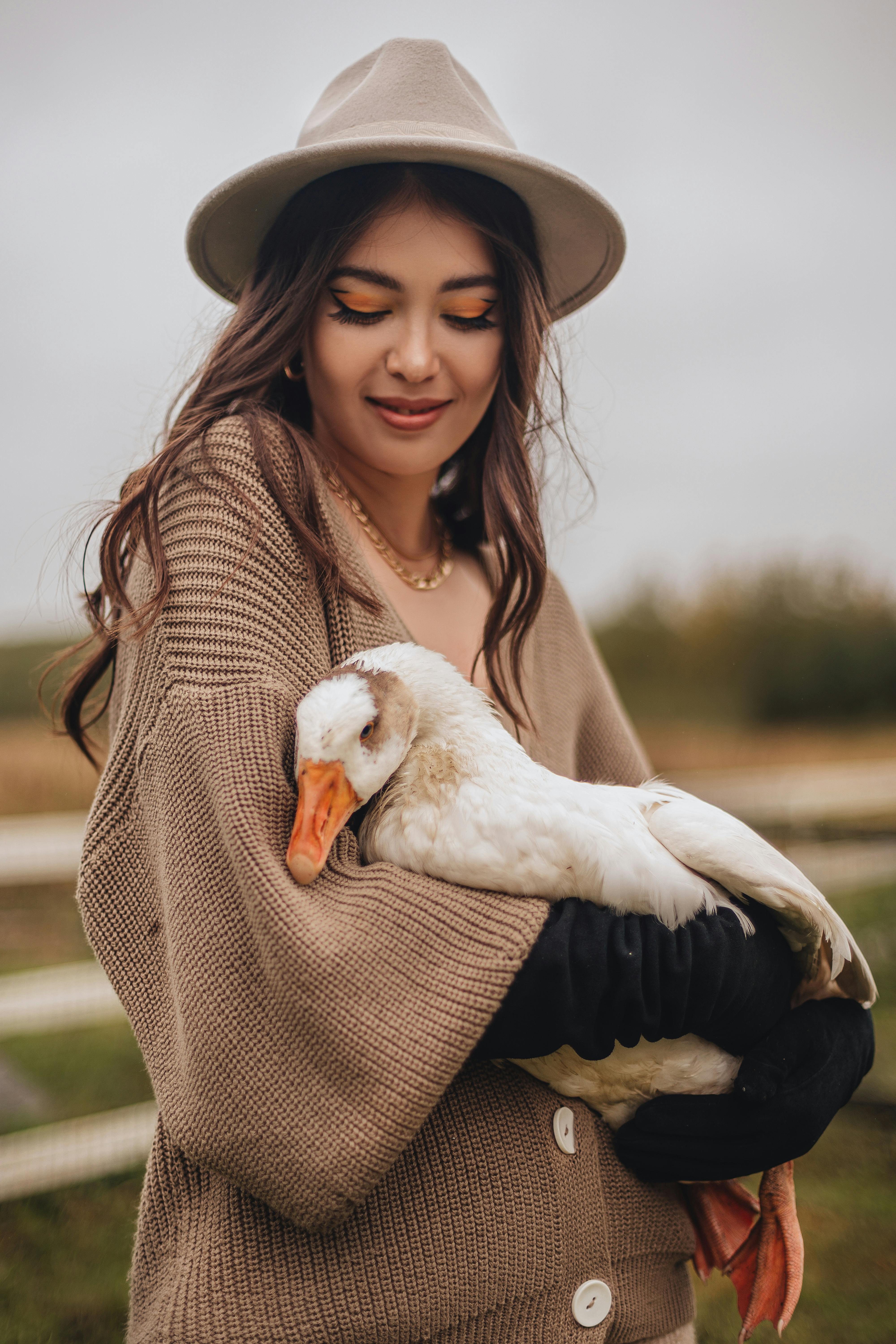 Photo of a Woman with a Hat Carrying a White Goose · Free Stock Photo