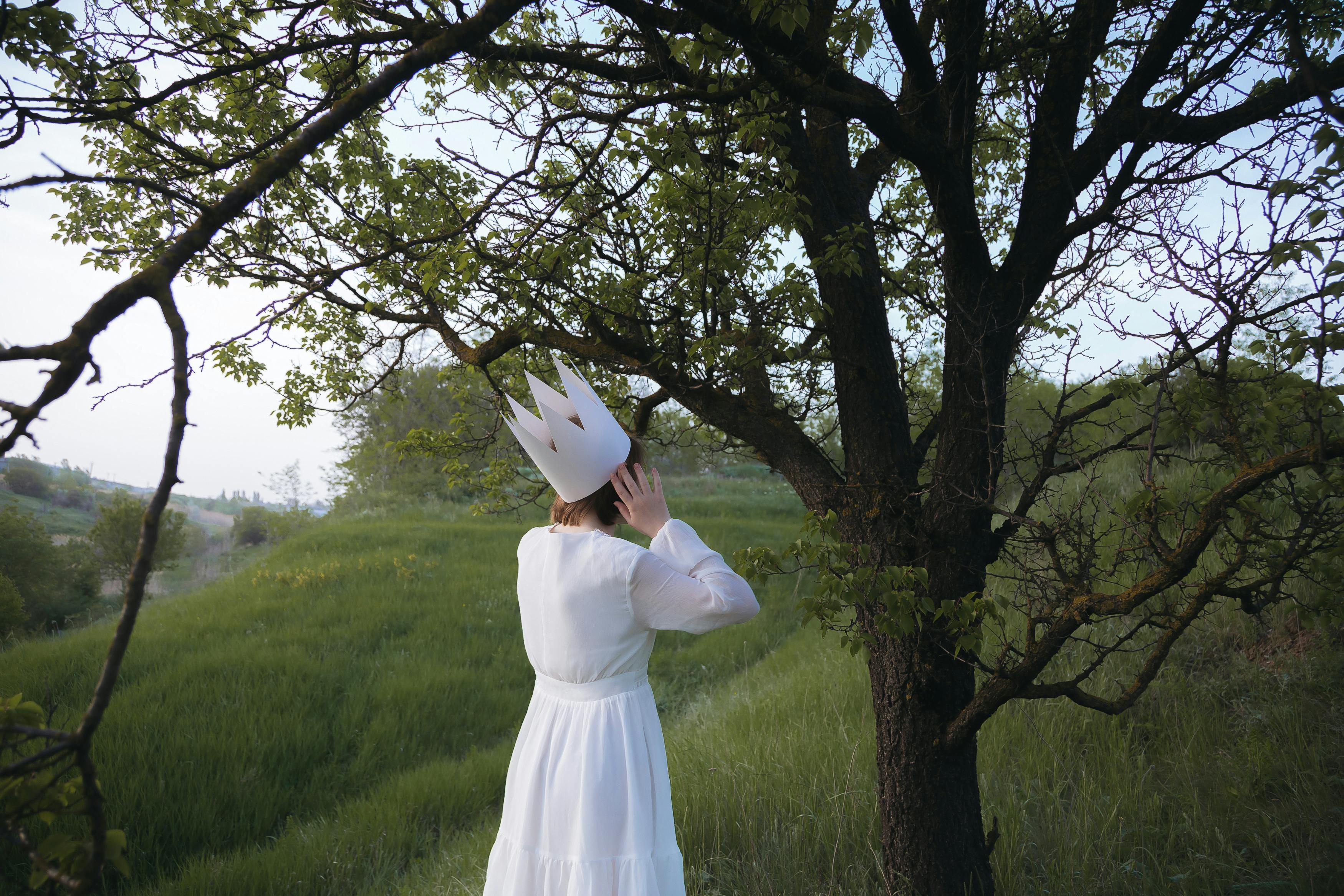 Woman in White Dress Wearing Paper Crown while Standing Under Green ...