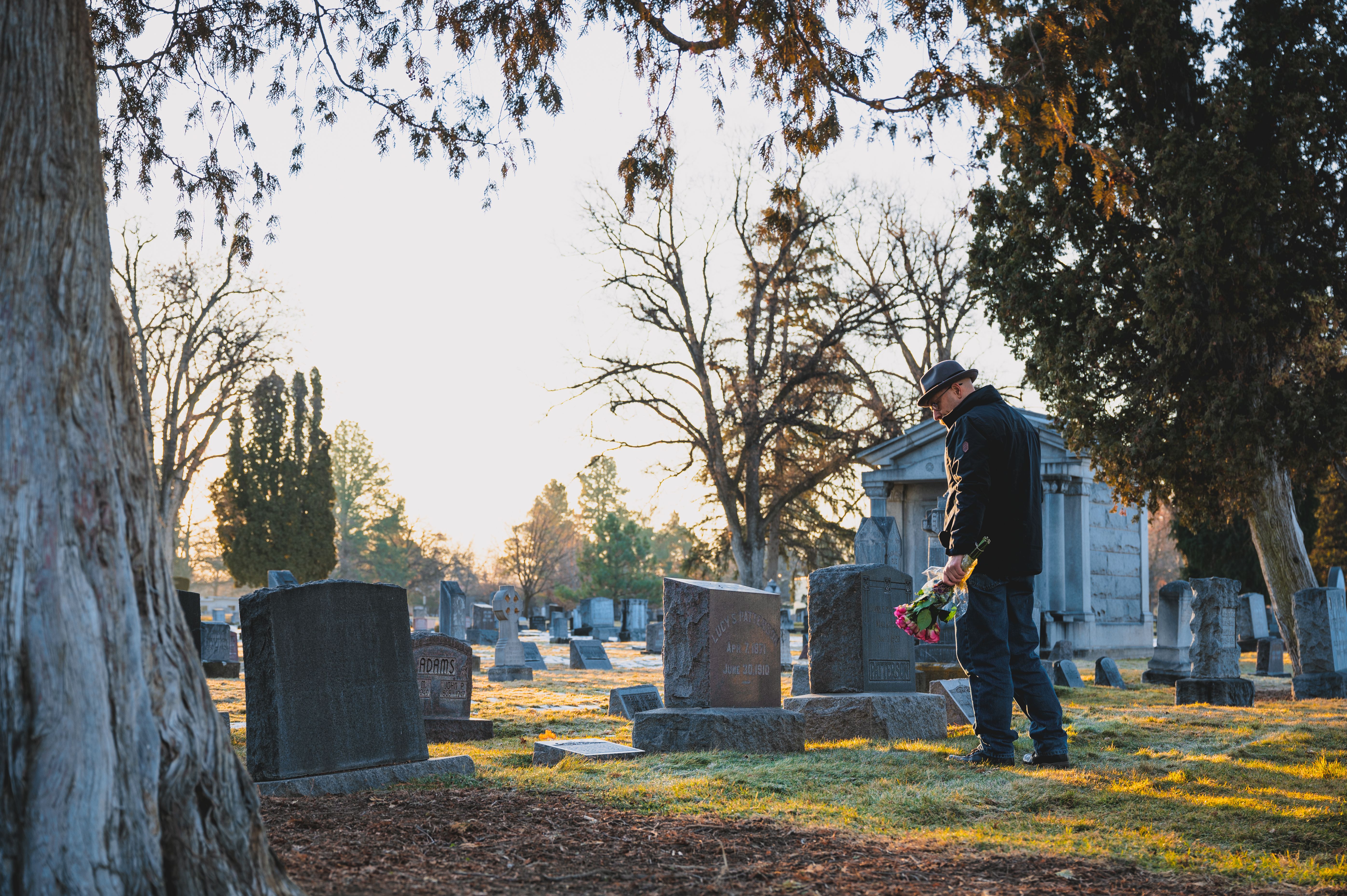 Man in Black Jacket Standing on the Grave while Holding Flowers · Free ...