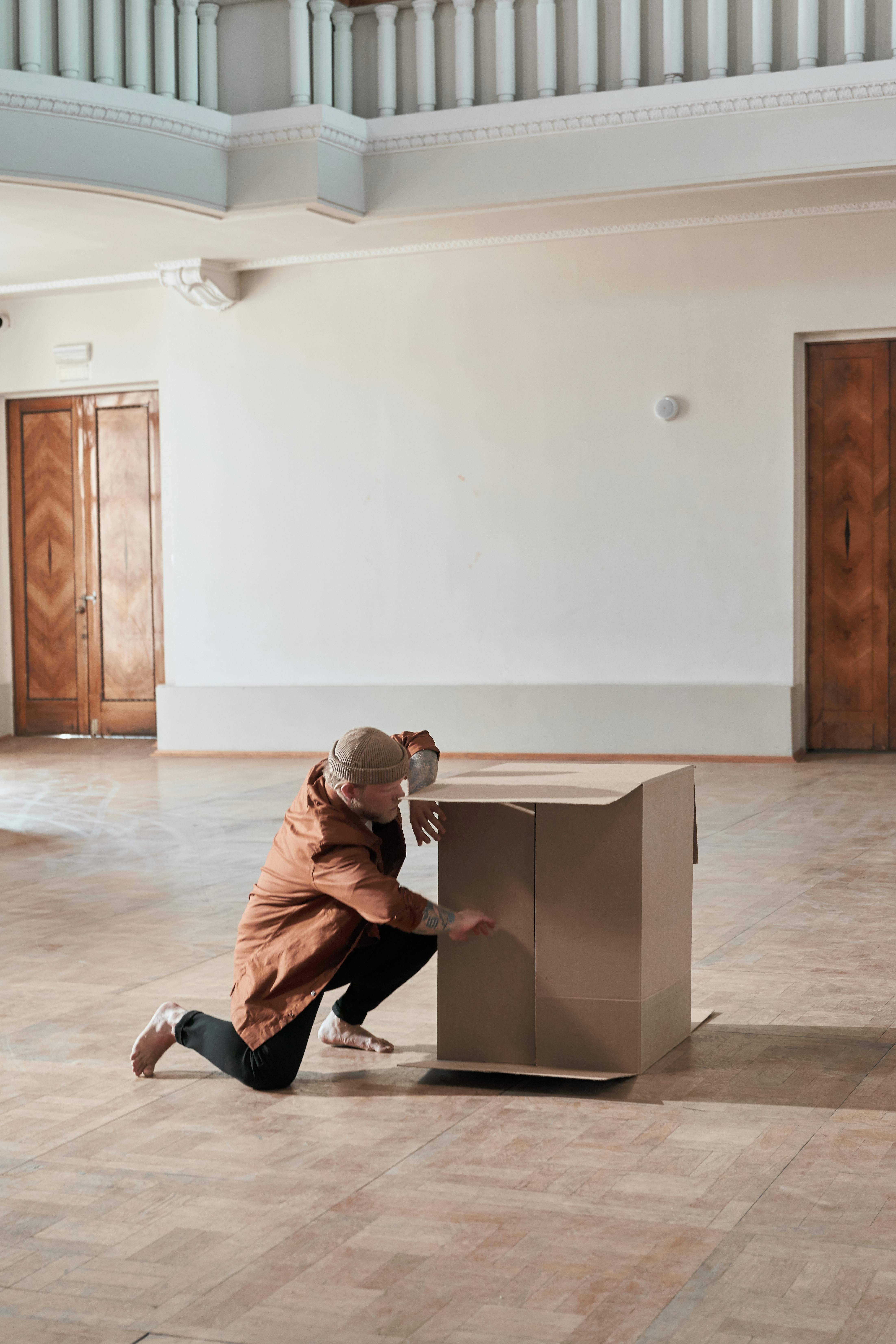 A Man Crouching Beside a Cardboard Box · Free Stock Photo