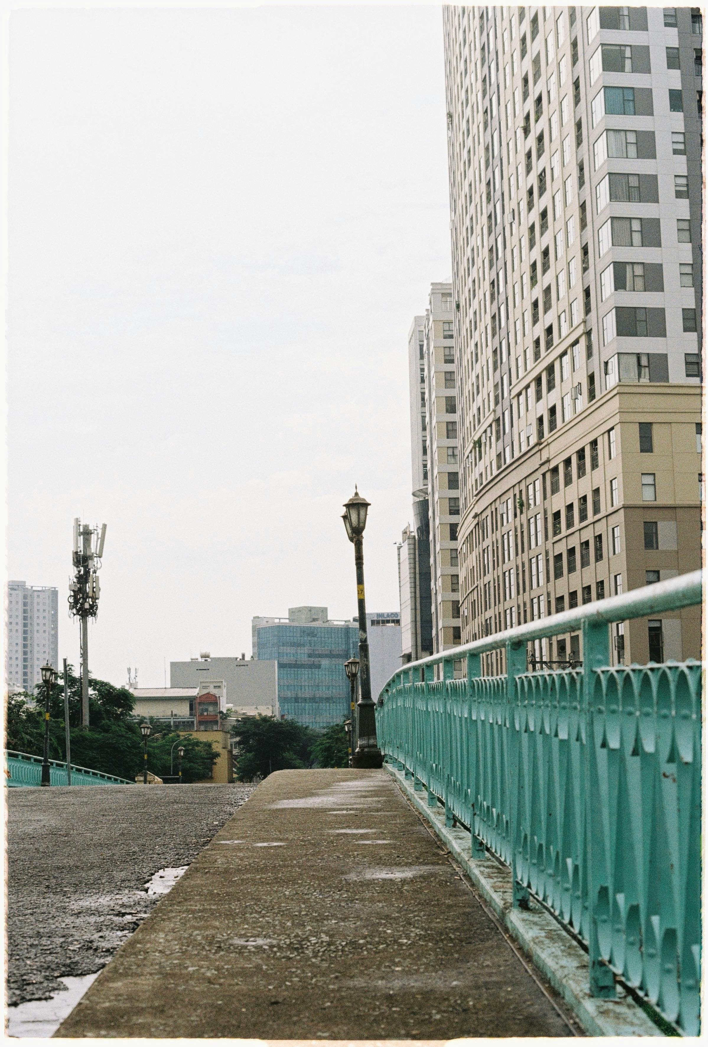 Green Metal Fence on Sidewalk Near High Rise Buildings · Free Stock Photo