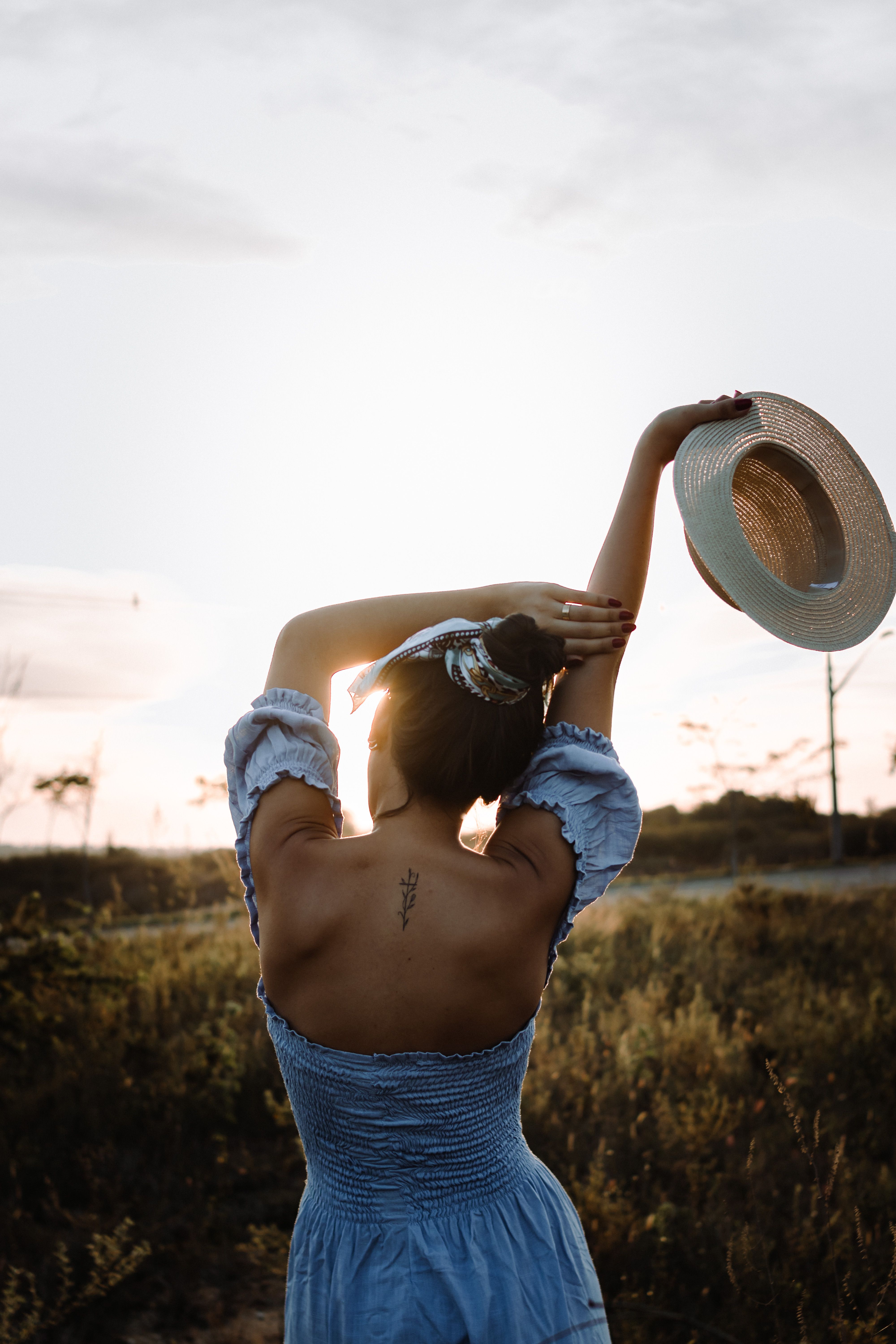 Back View of a Woman in Light Blue Dress Holding a Sun Hat during ...