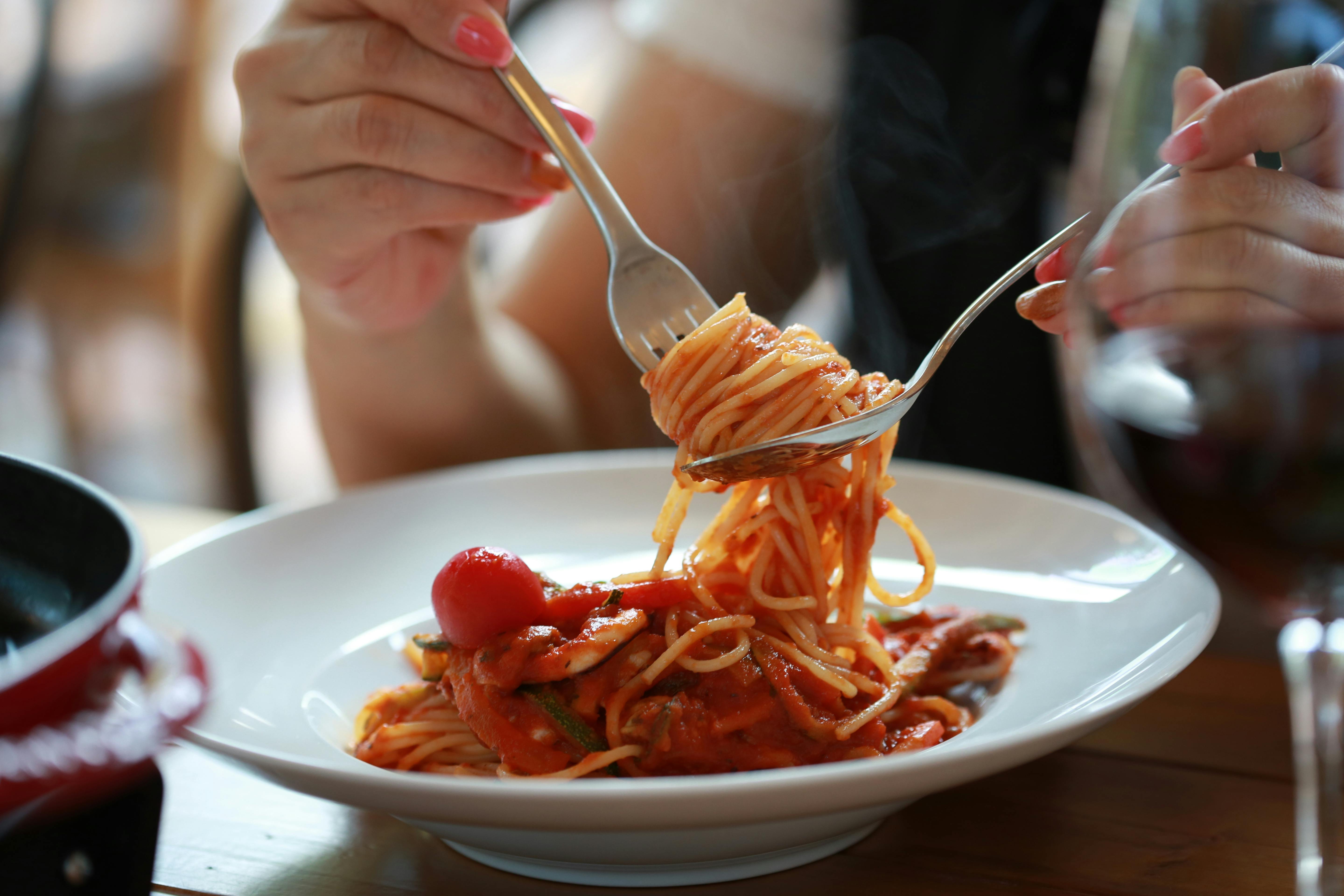 A Person Holding a Spoon and Fork with Spaghetti · Free Stock Photo