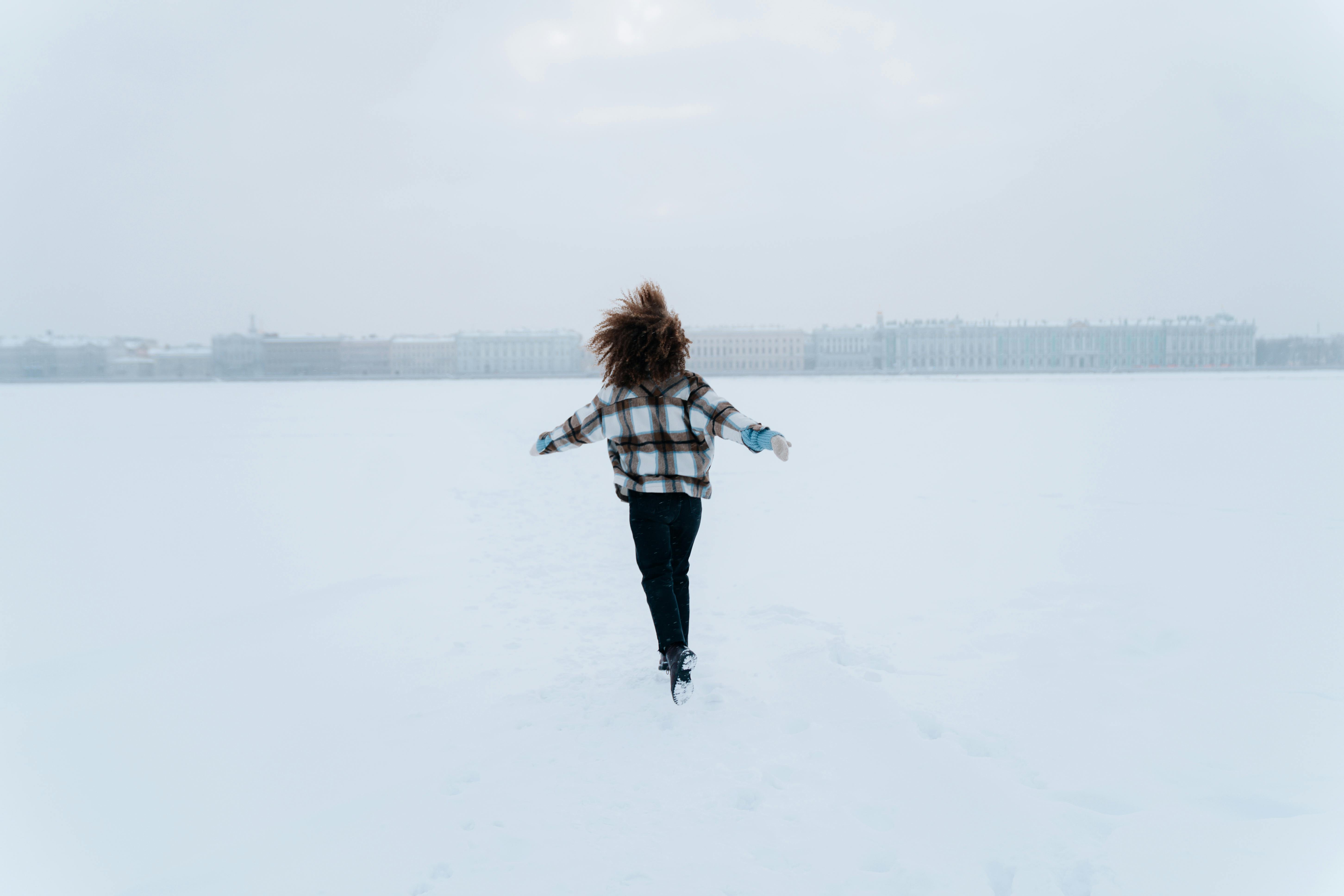 Woman Running Through Snow Field with Arms Stretched out · Free Stock Photo