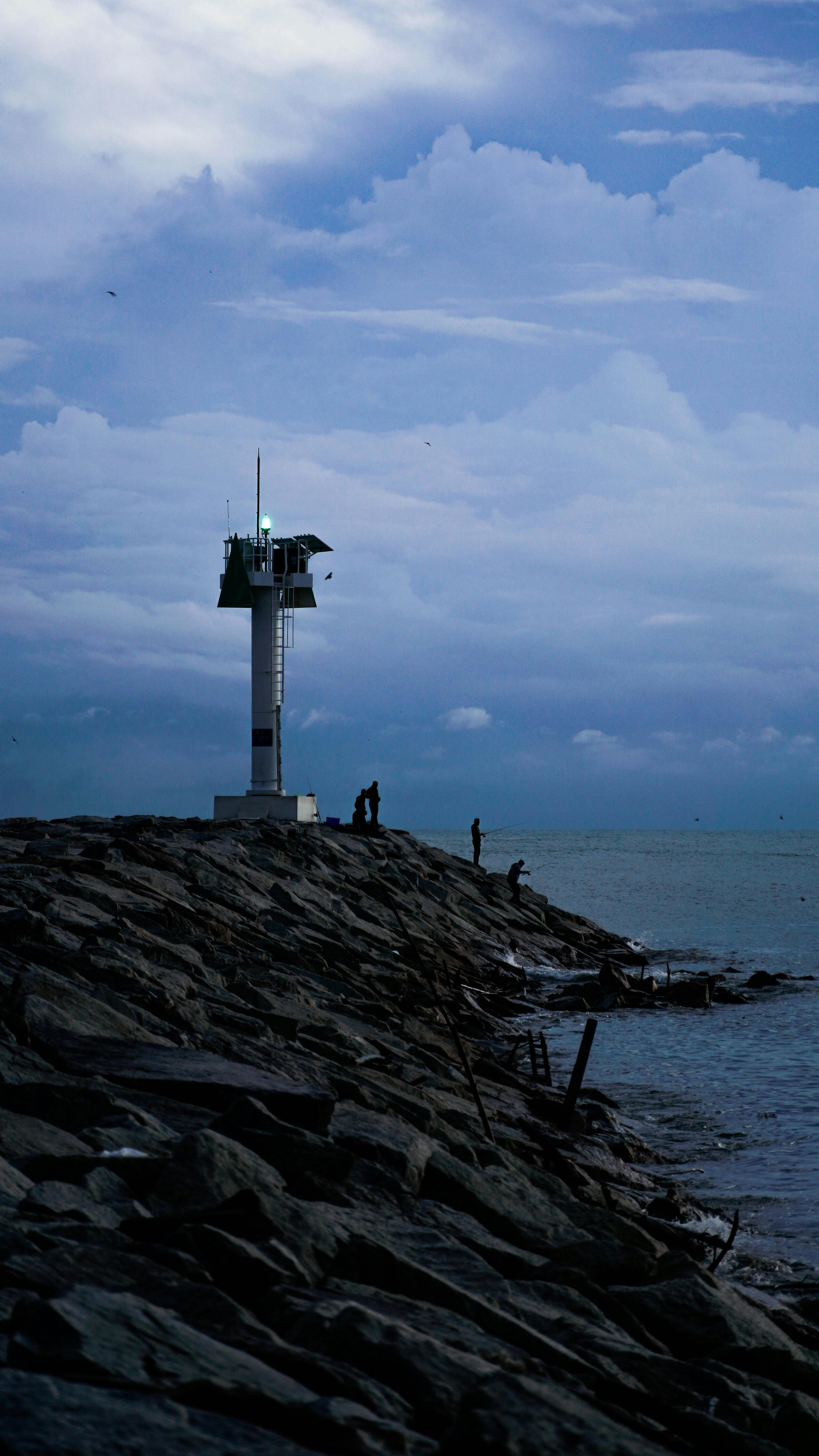 White and Black Lighthouse on Gray Rock Formation Near Body of Water ...