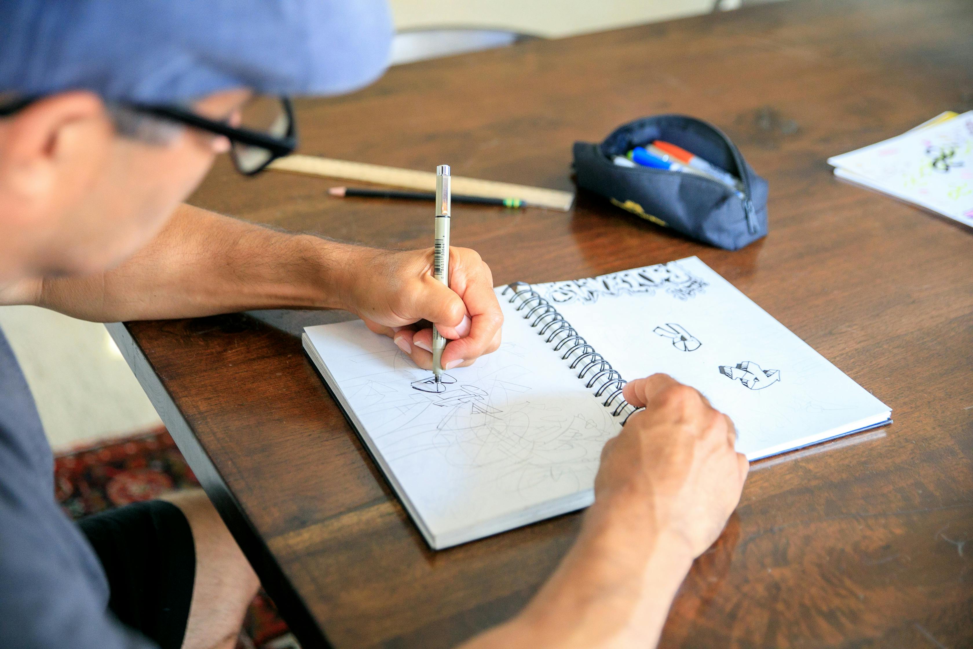 Man Drawing in Spiral Notebook · Free Stock Photo