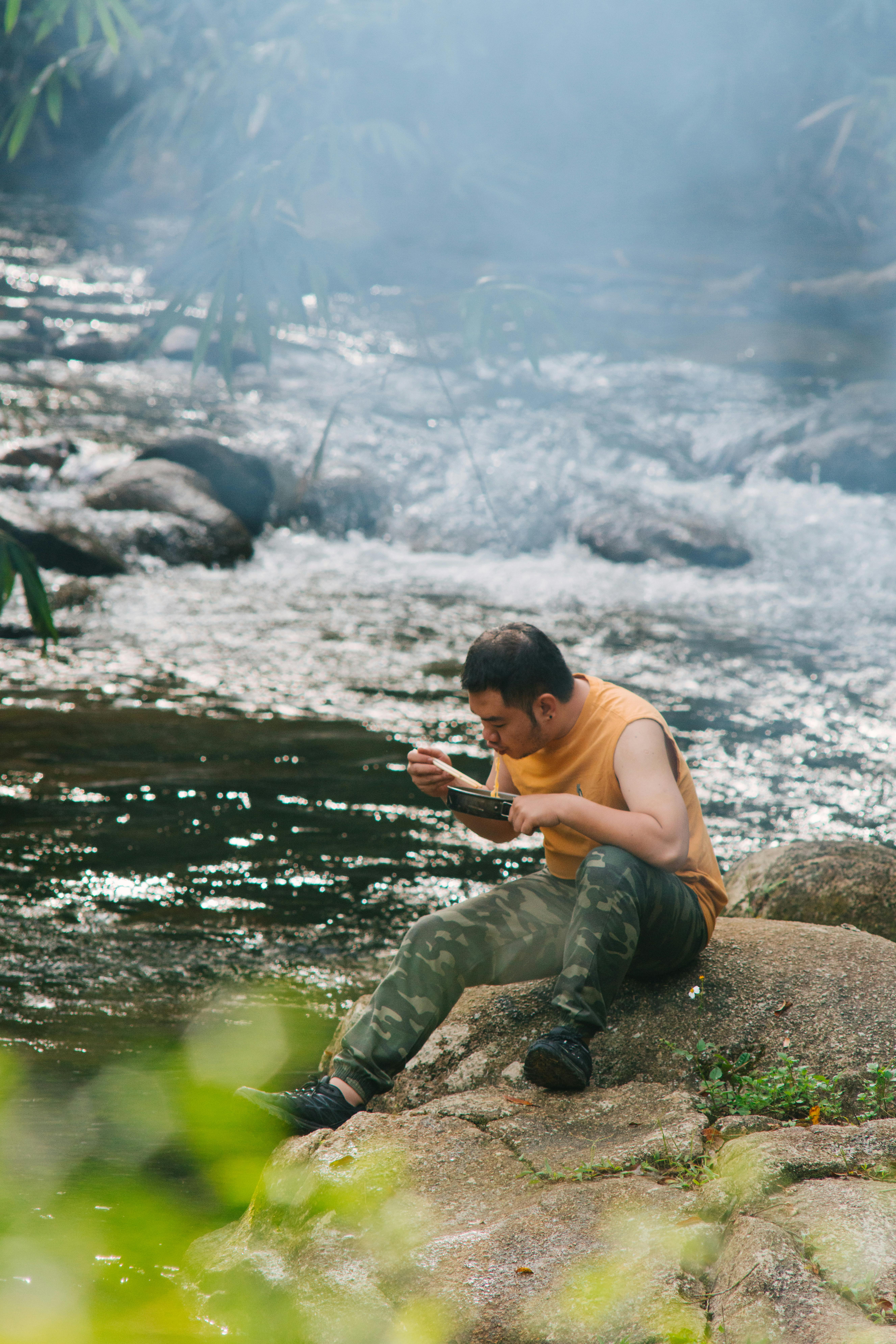 Man Sitting on Rock by River and Eating · Free Stock Photo