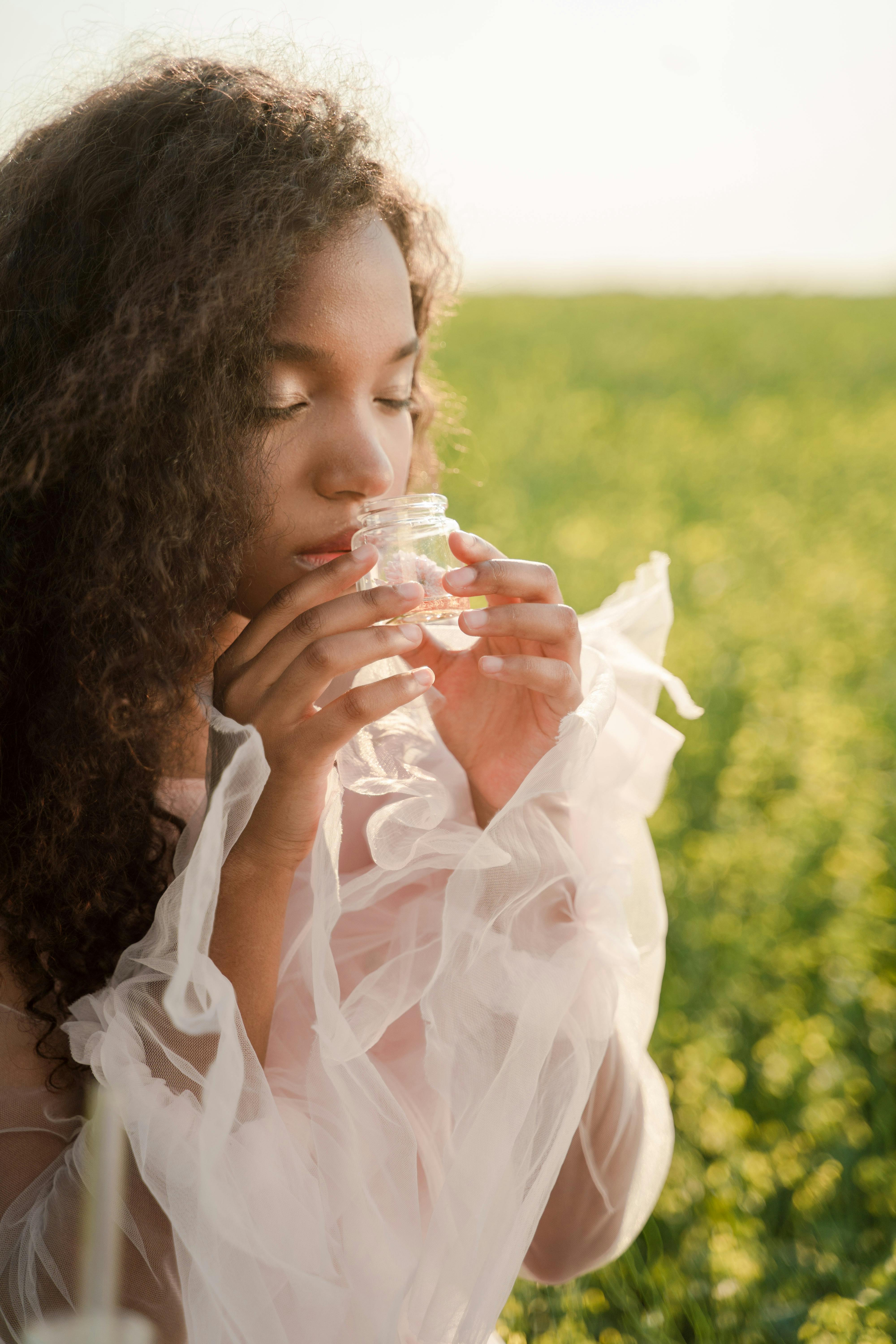Woman on a Meadow Smelling a Liquid in a Glass · Free Stock Photo