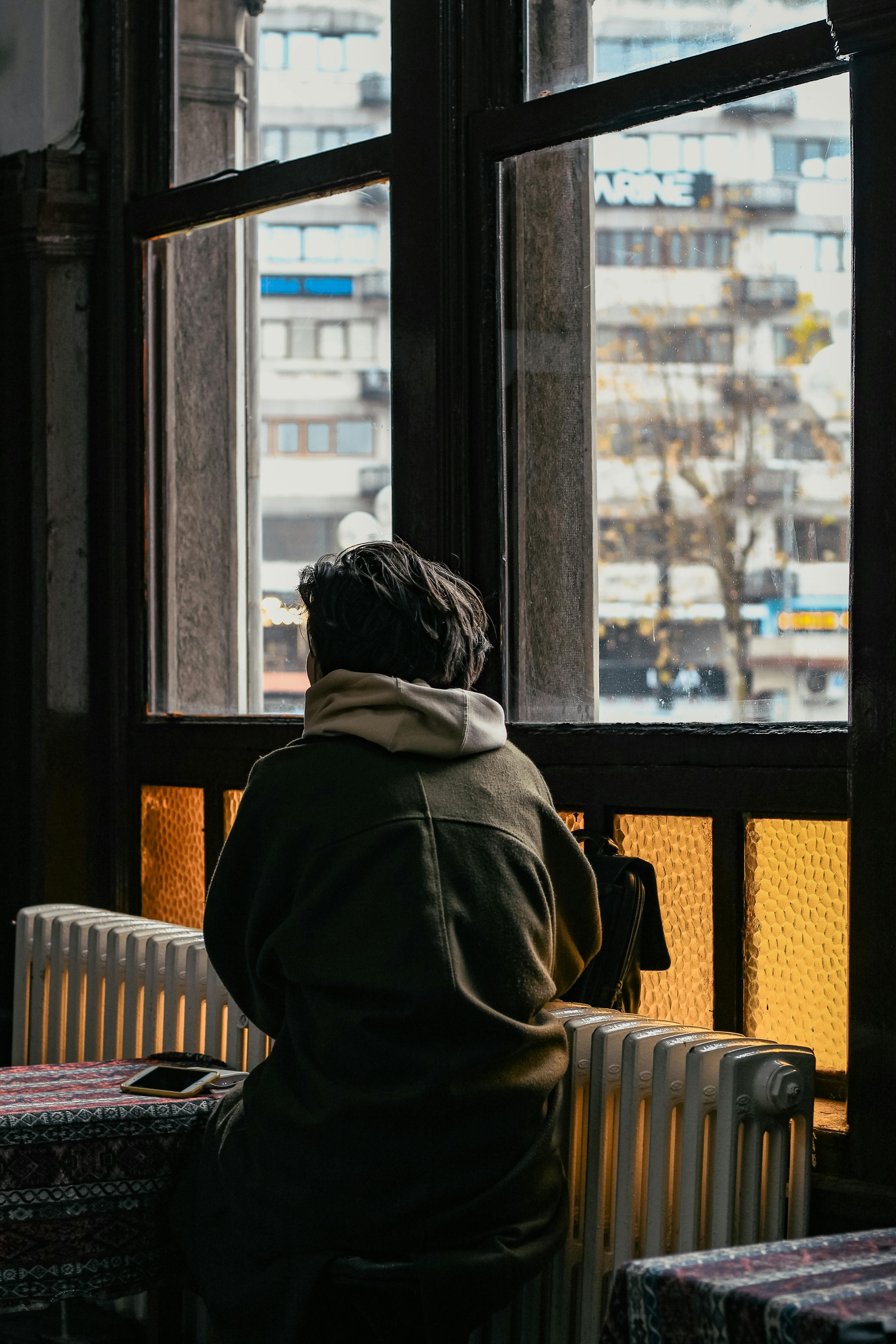 Person in Brown Hoodie Sitting on Chair Near Glass Window · Free Stock ...