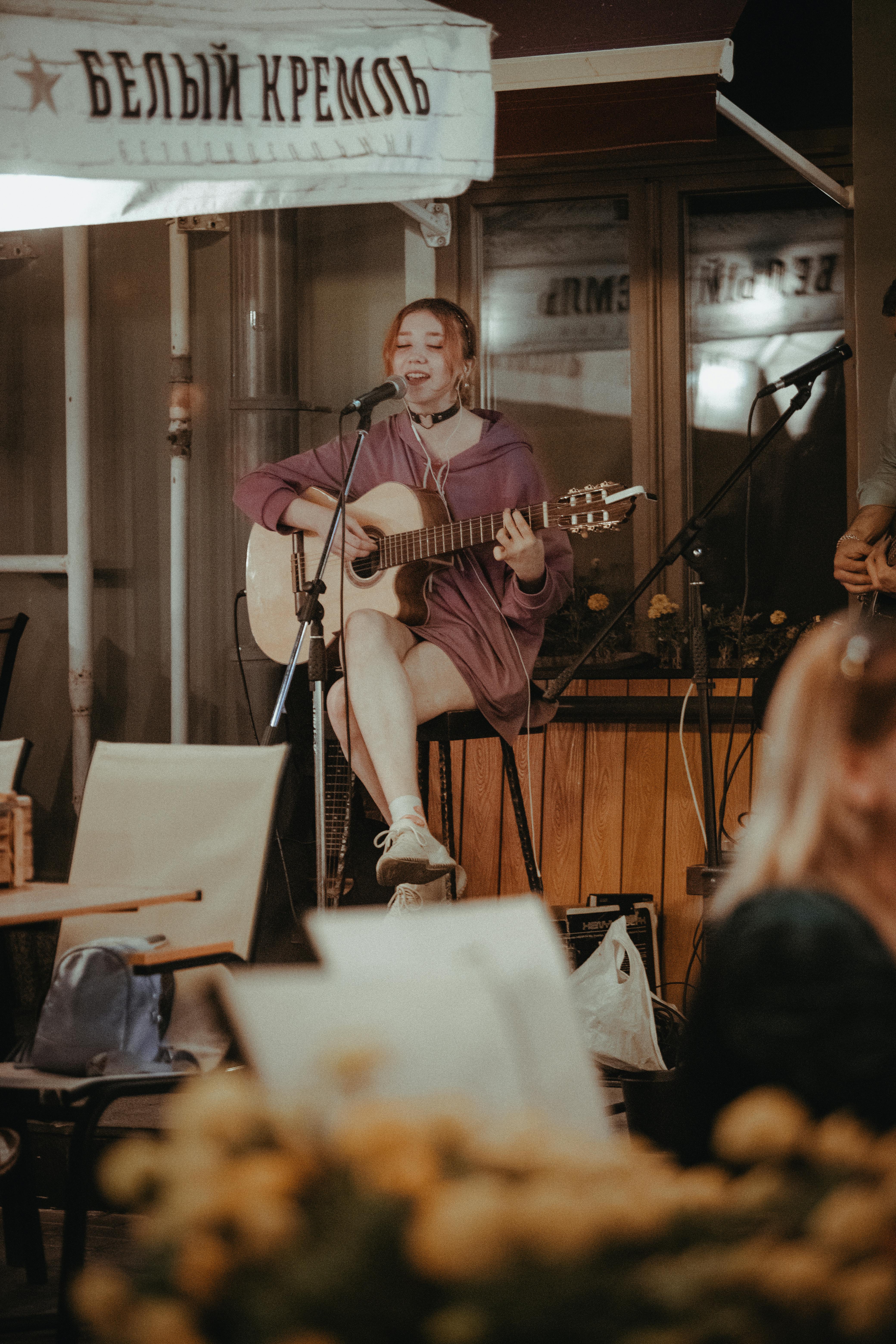 A Woman Singing while Playing Guitar on Stage · Free Stock Photo