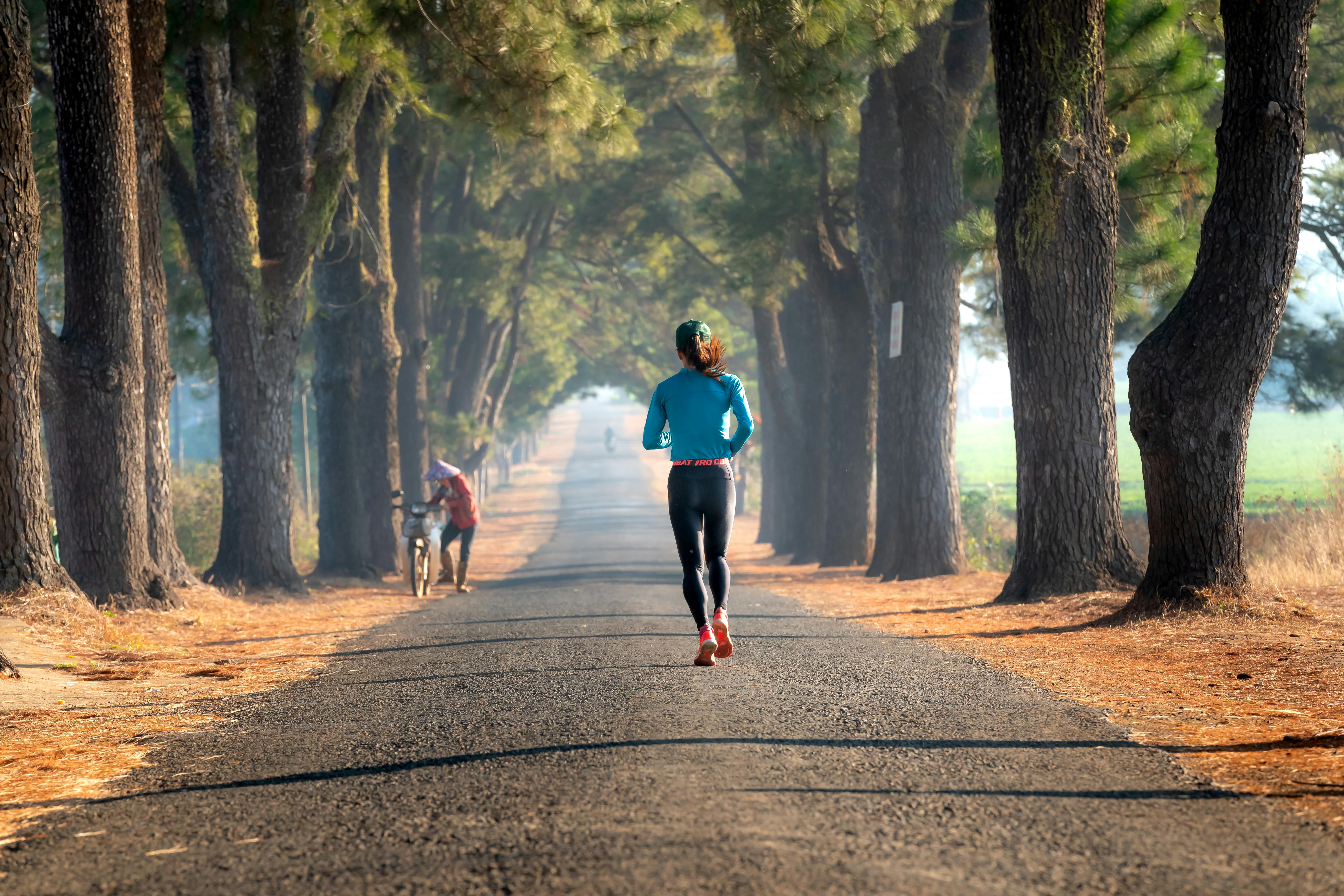 A Back View of a Woman in Black Leggings Running on a Concrete Road ...