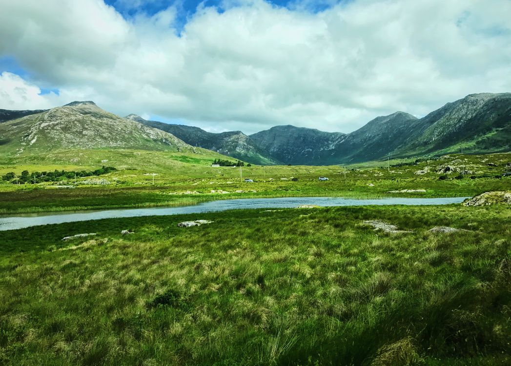 Green Grass Field near Mountains under the Cloudy Sky · Free Stock Photo