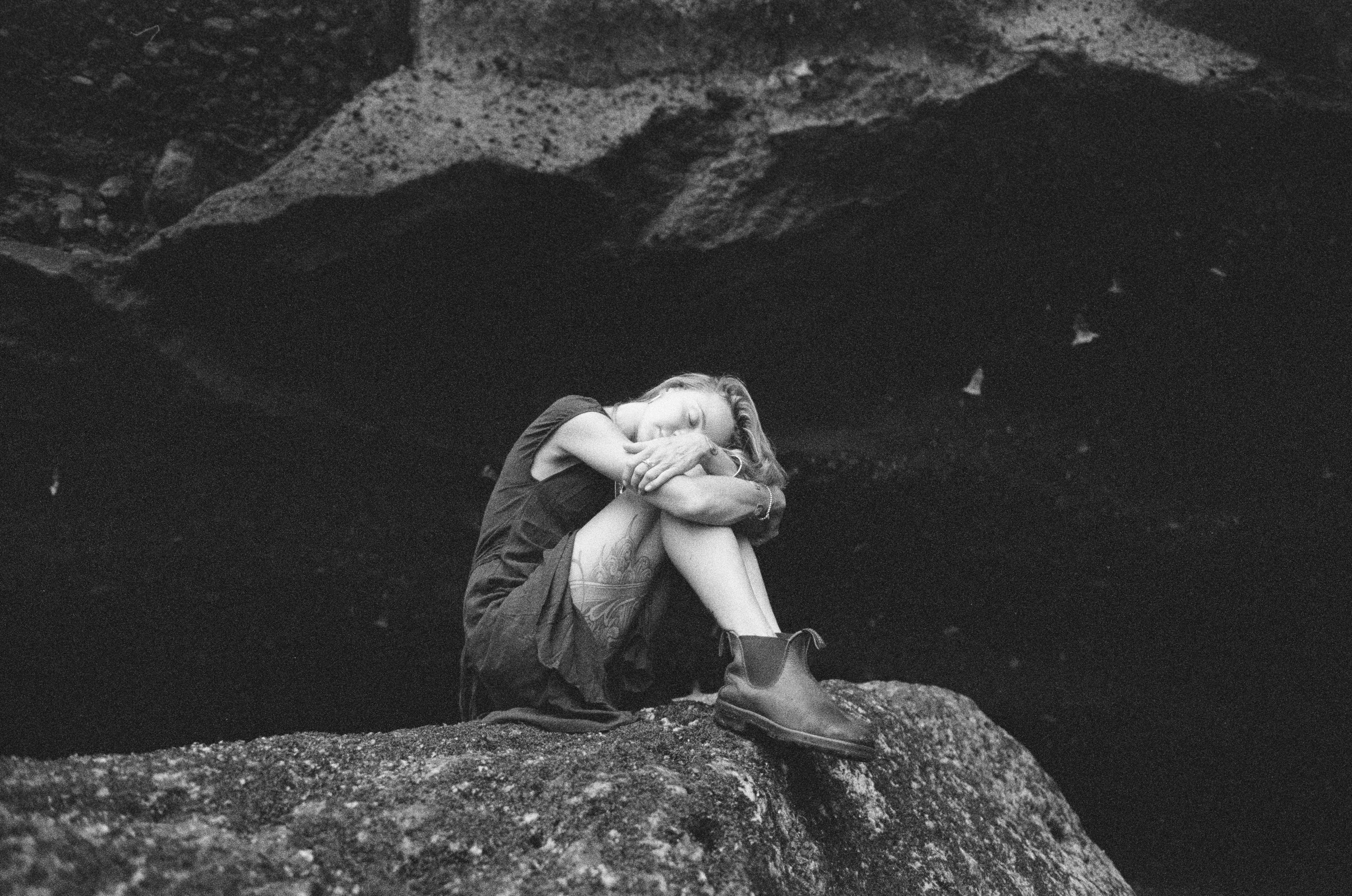 Grayscale Photo of a Woman in Black Dress Sitting on Rock · Free Stock ...