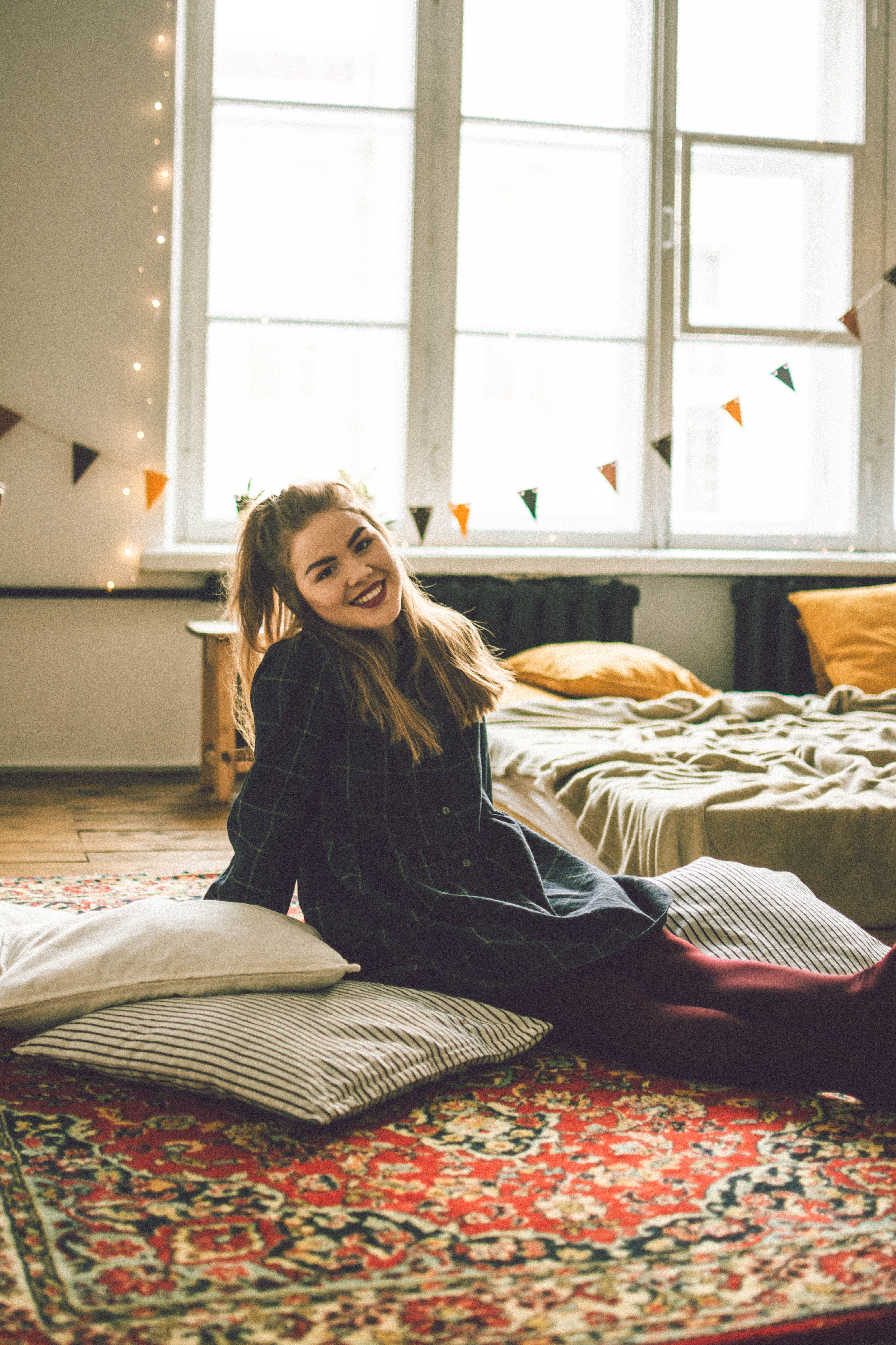 Smiling Girl Sitting on Rug and Pillows · Free Stock Photo