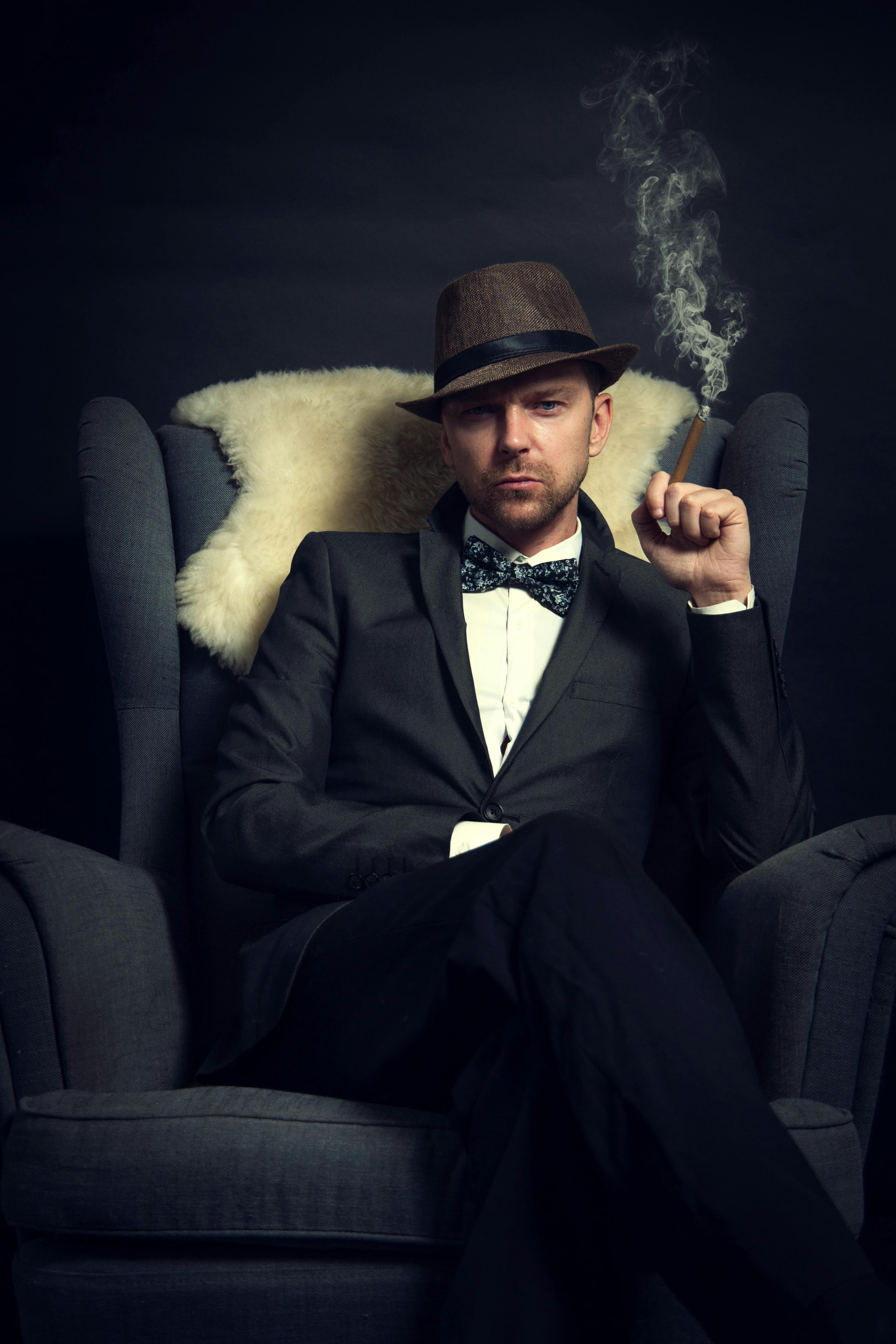 Photo of Man in Black Suit Sitting on White Couch Smoking a Cigar ...