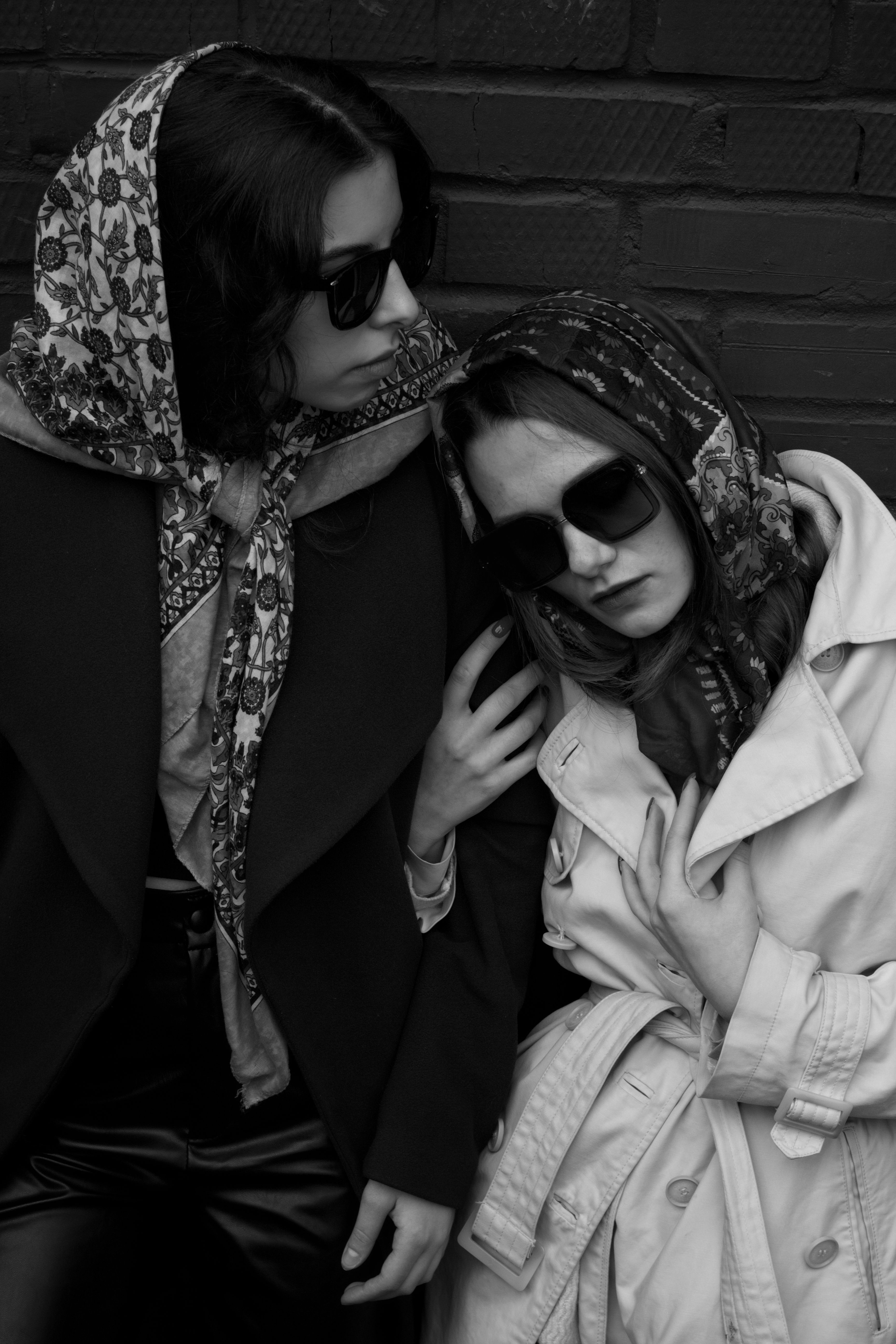 Two Young Women in Headscarves and Sunglasses Sitting with Linked Arms ...