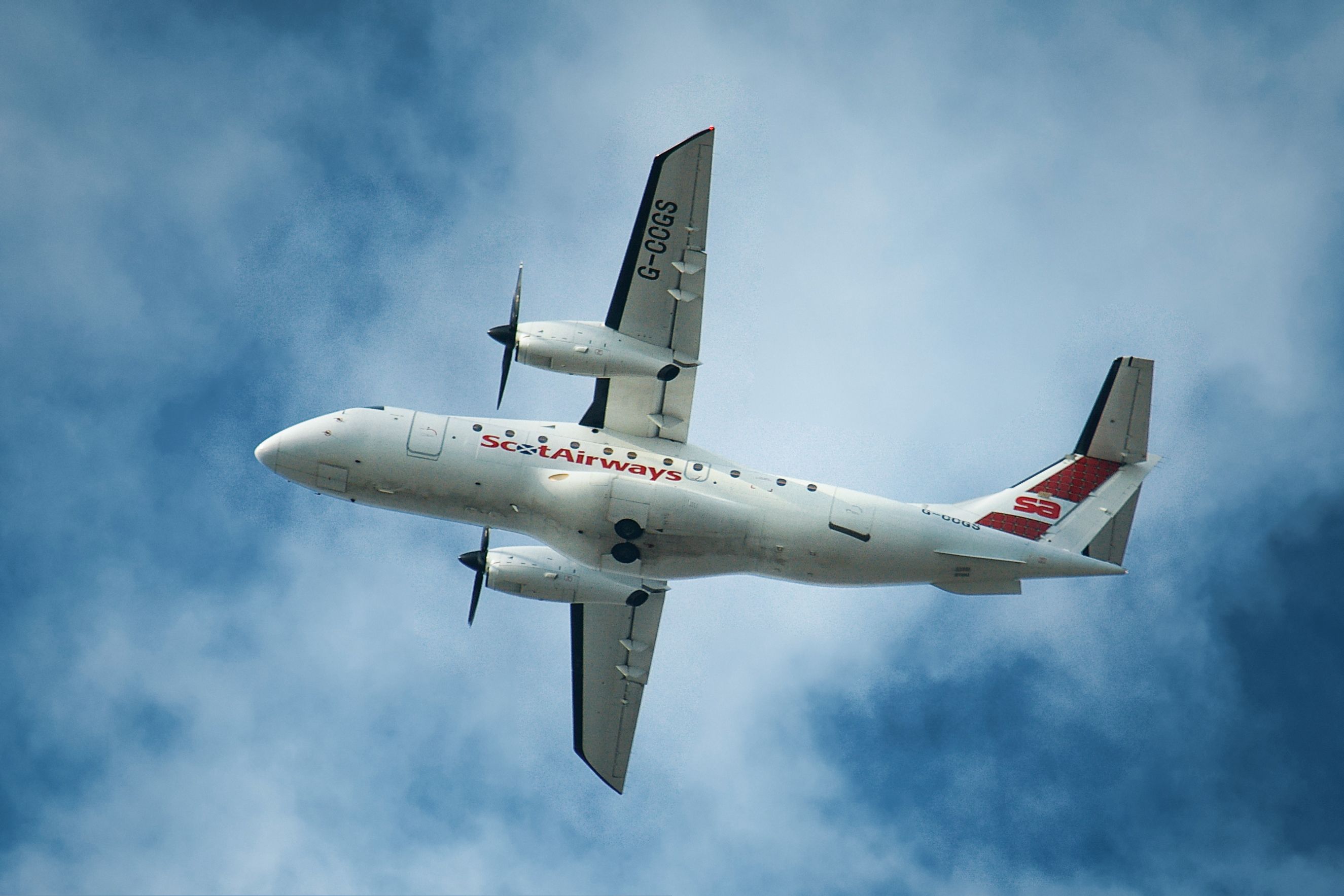 White and Blue Airplane Flying Under Cloudy Sky · Free Stock Photo