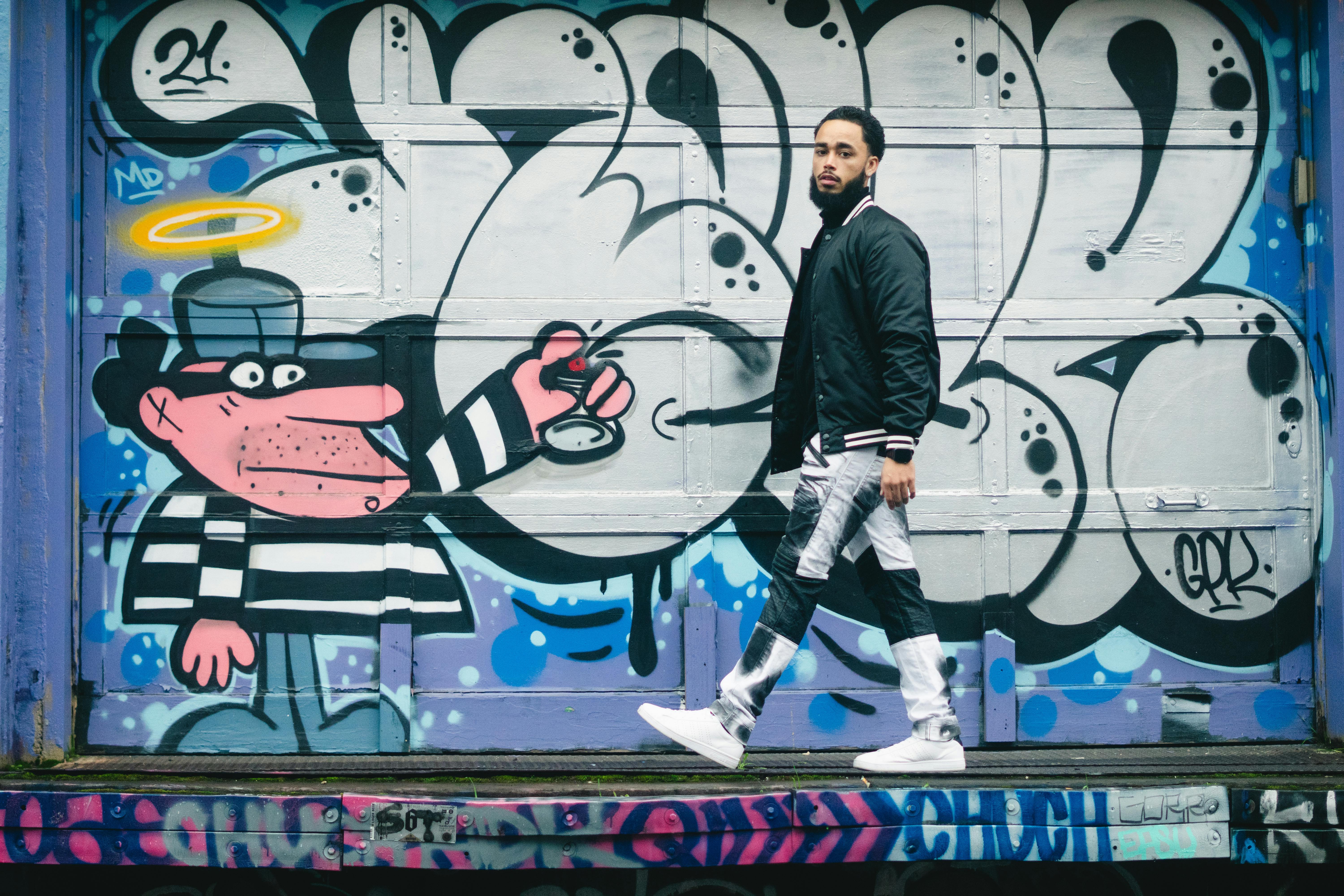 Young Man Walking on the Background of a Graffiti Wall · Free Stock Photo