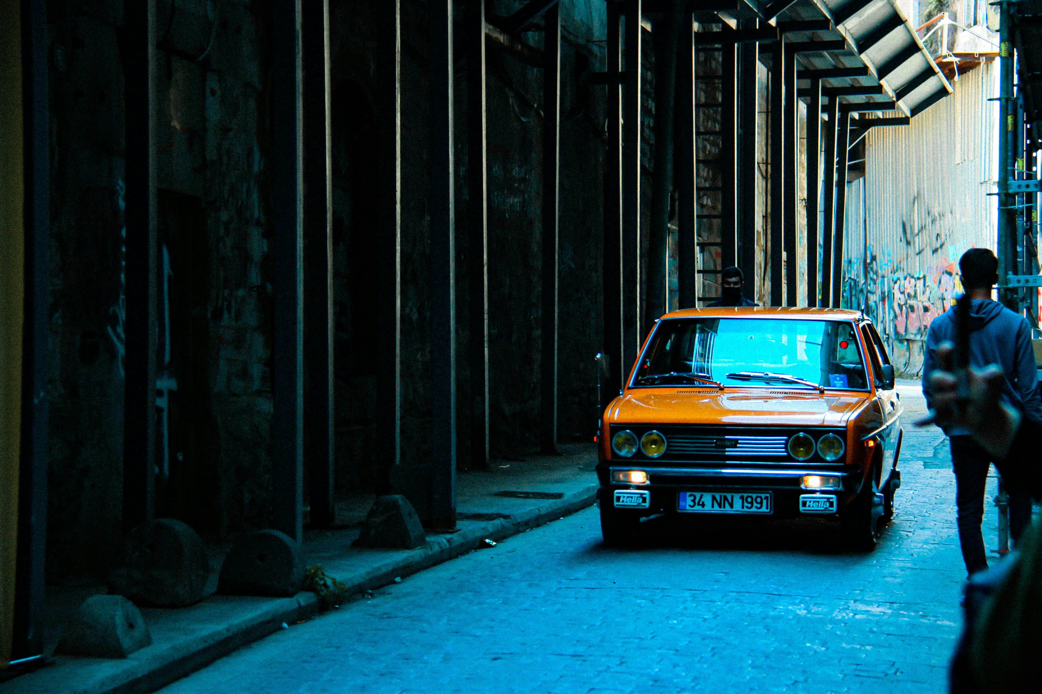 A Man Walking Down a Slanting Road with Parked Cars · Free Stock Photo