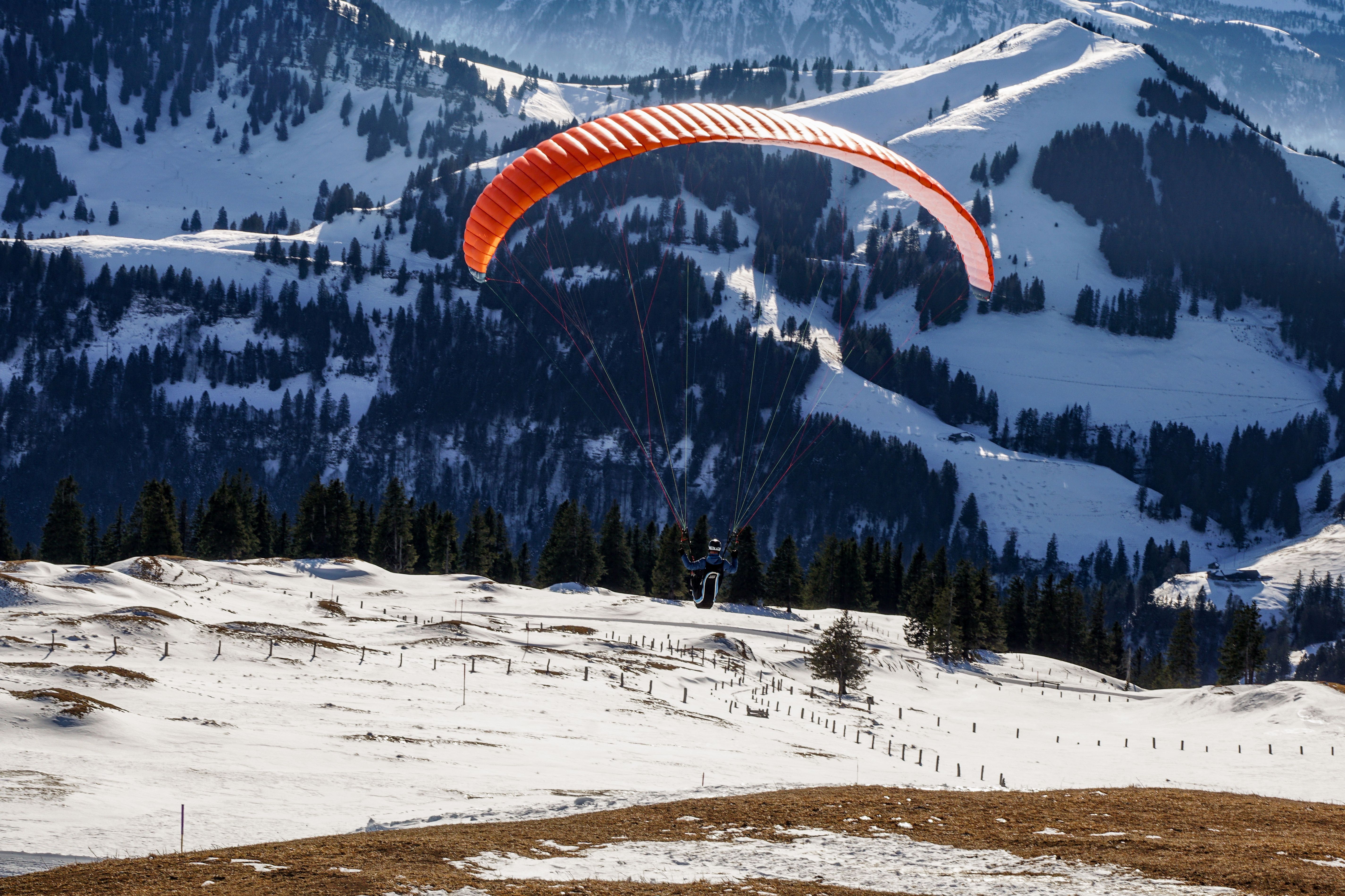 Person Paragliding Over Snow Covered Ground · Free Stock Photo