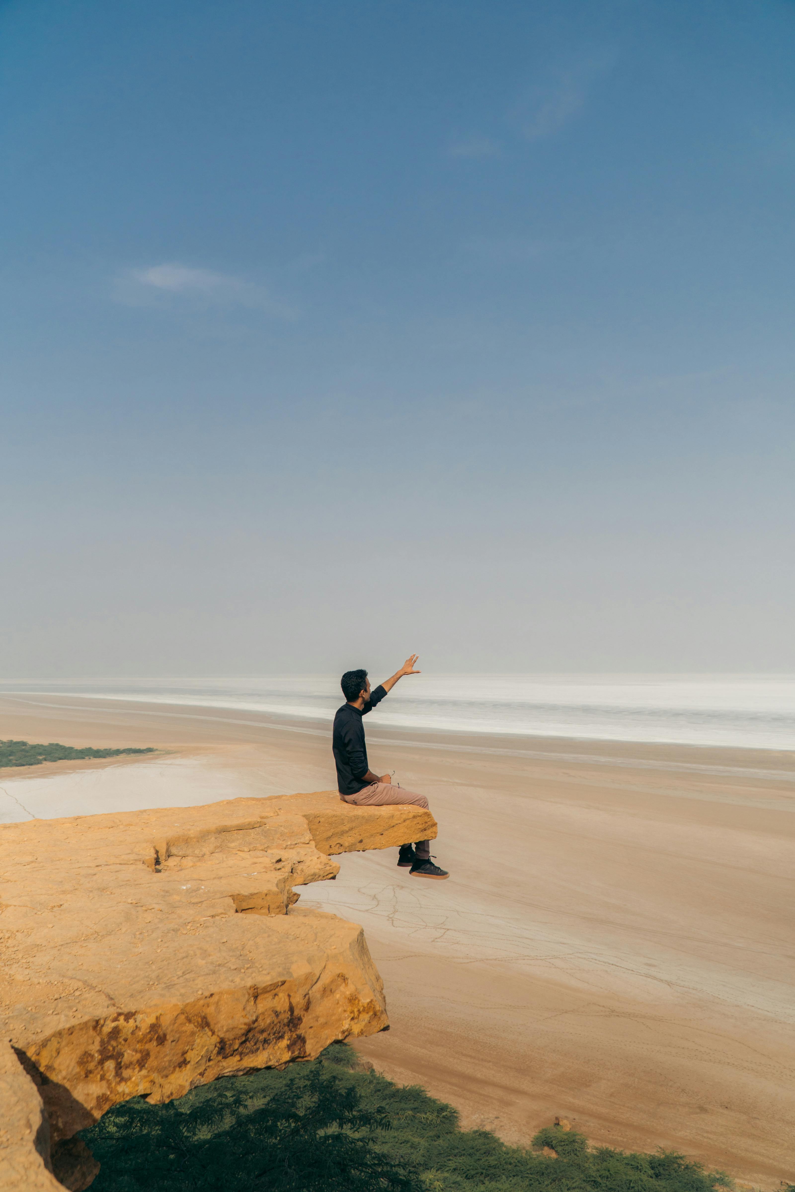 Man Sitting on Edge of Protruding Cliff Rock · Free Stock Photo
