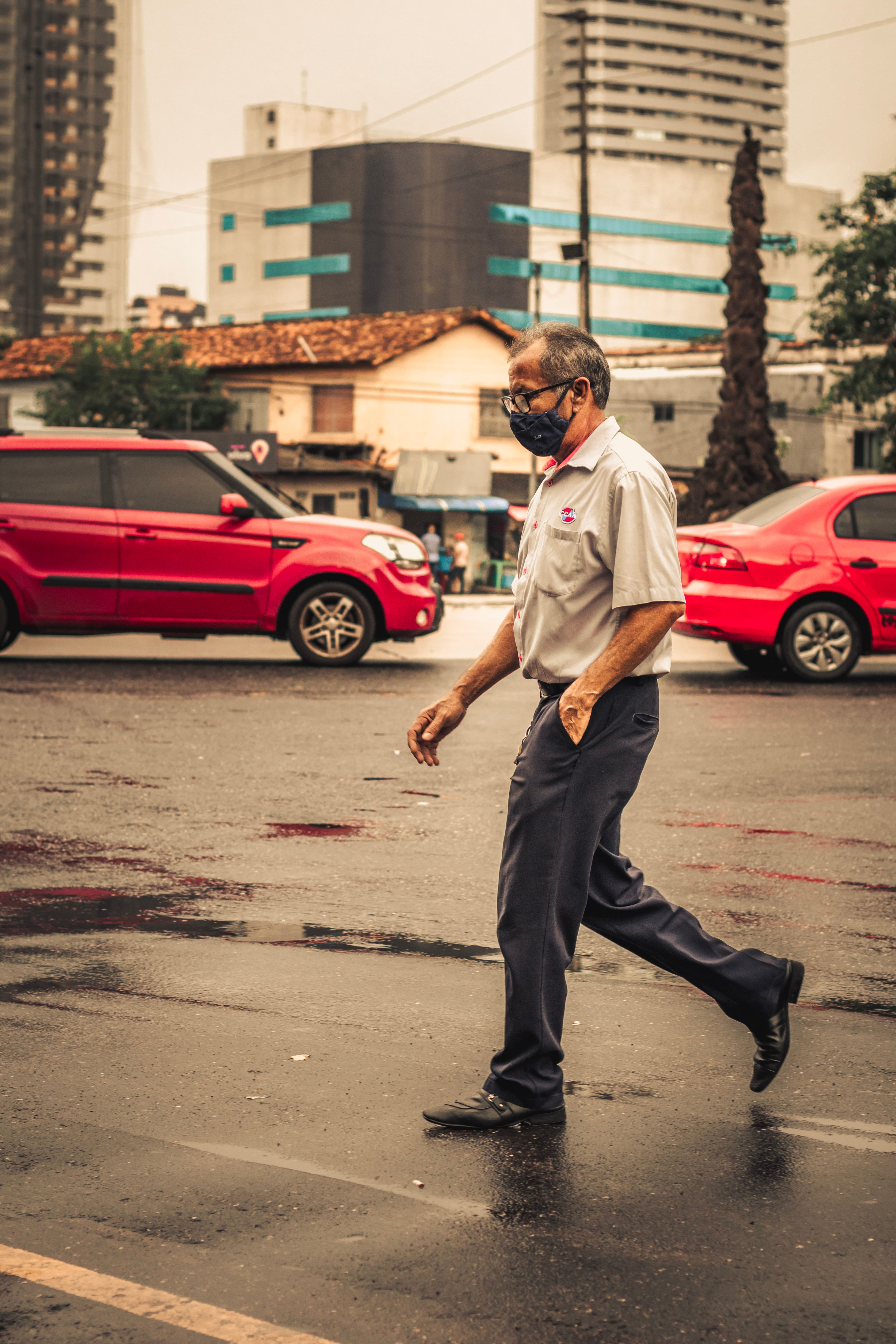 A Man Walking on a Wet Road Wearing Face Mask · Free Stock Photo