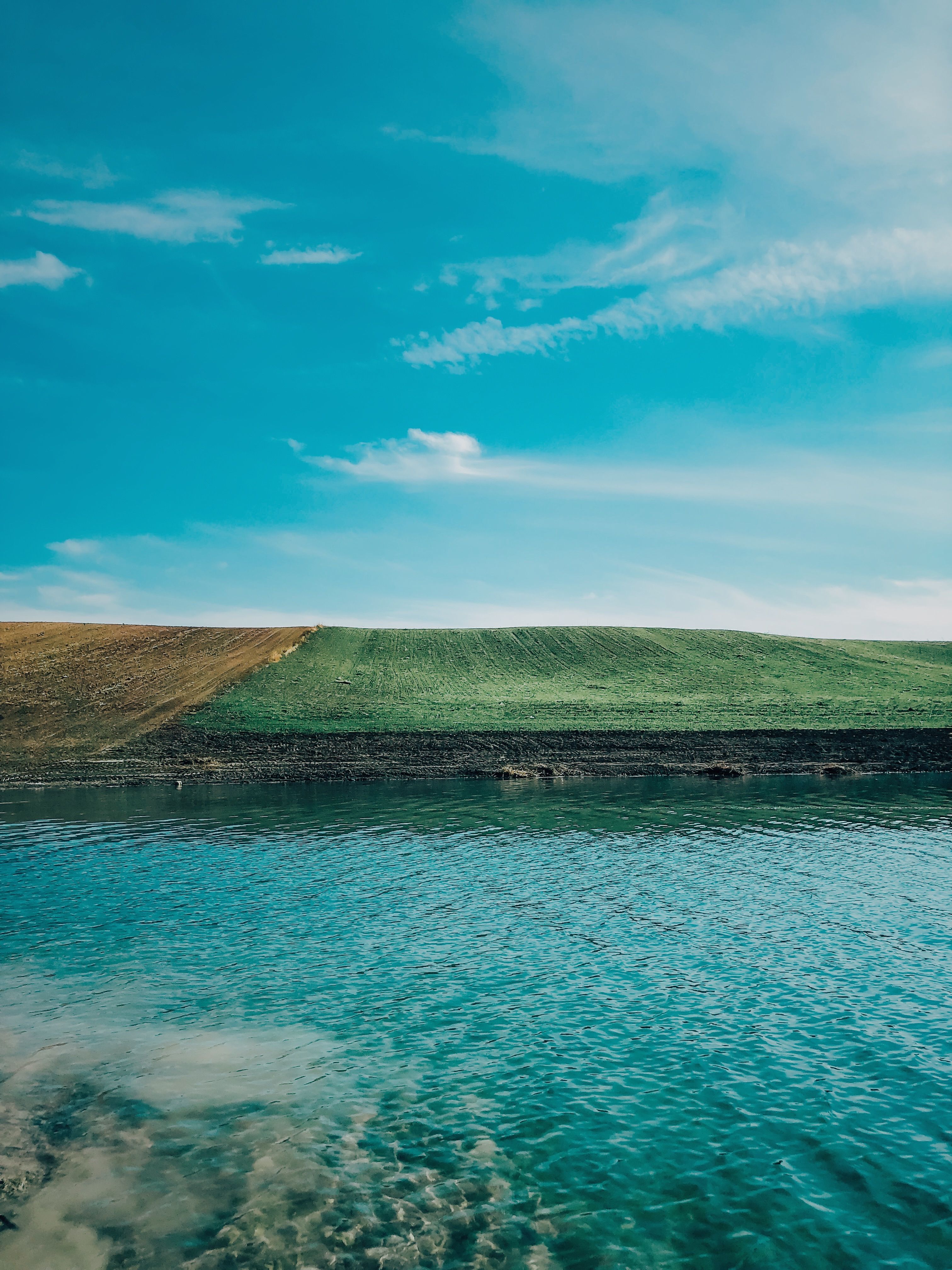 Green Grass Field Near Lake Under Blue Sky · Free Stock Photo