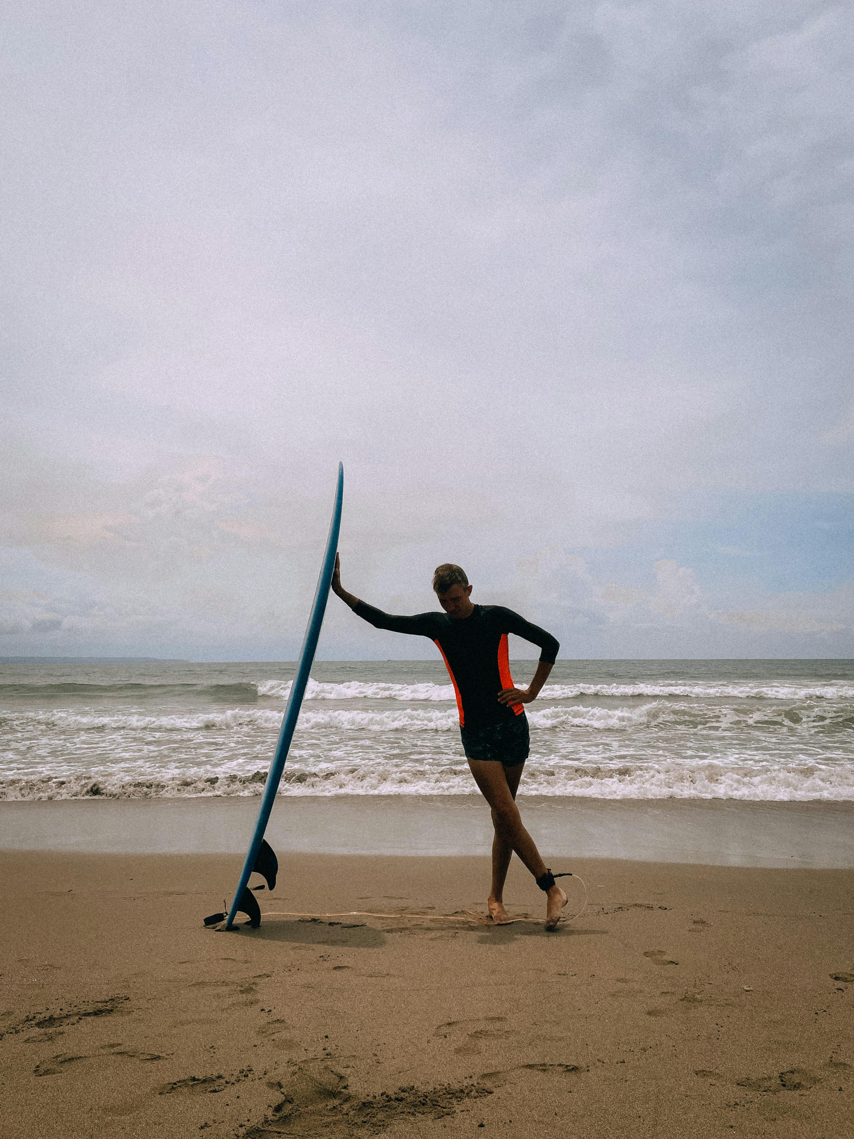 A Man in Black Rash Guard Standing Near the Surfboard · Free Stock Photo
