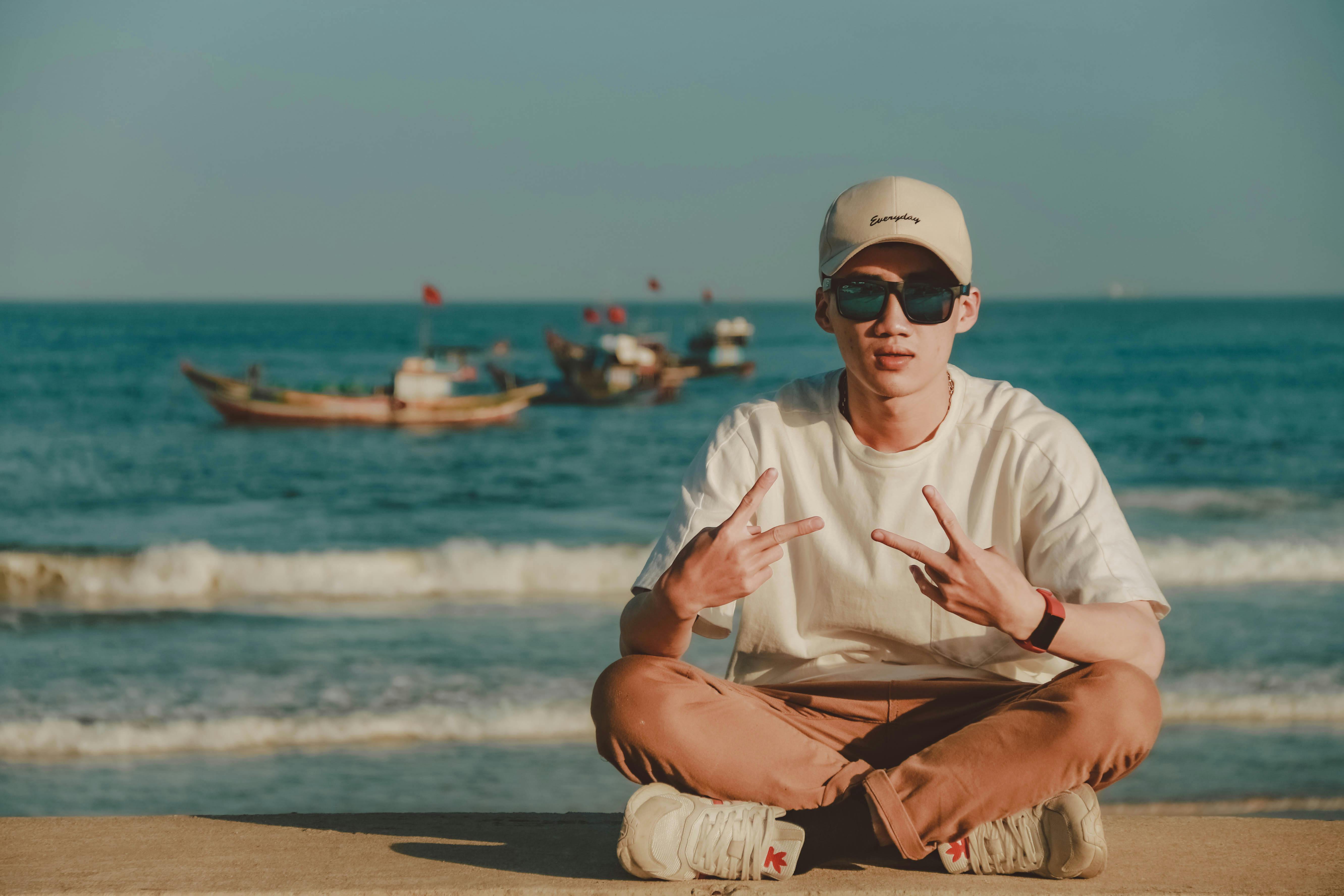 Man Sitting on Shore Doing a Peace Sign · Free Stock Photo