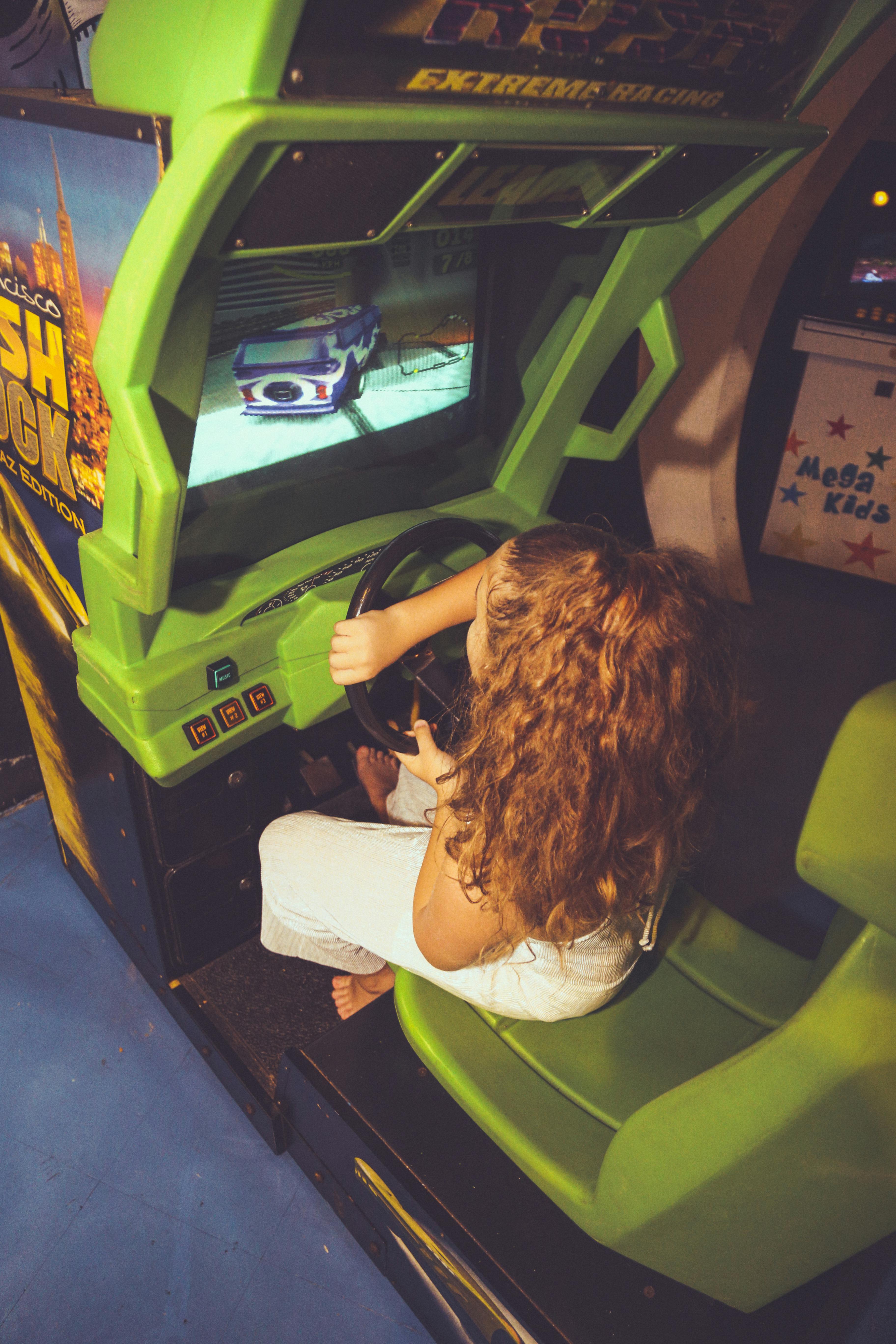 A Girl in White Clothes Playing on an Arcade Ride · Free Stock Photo