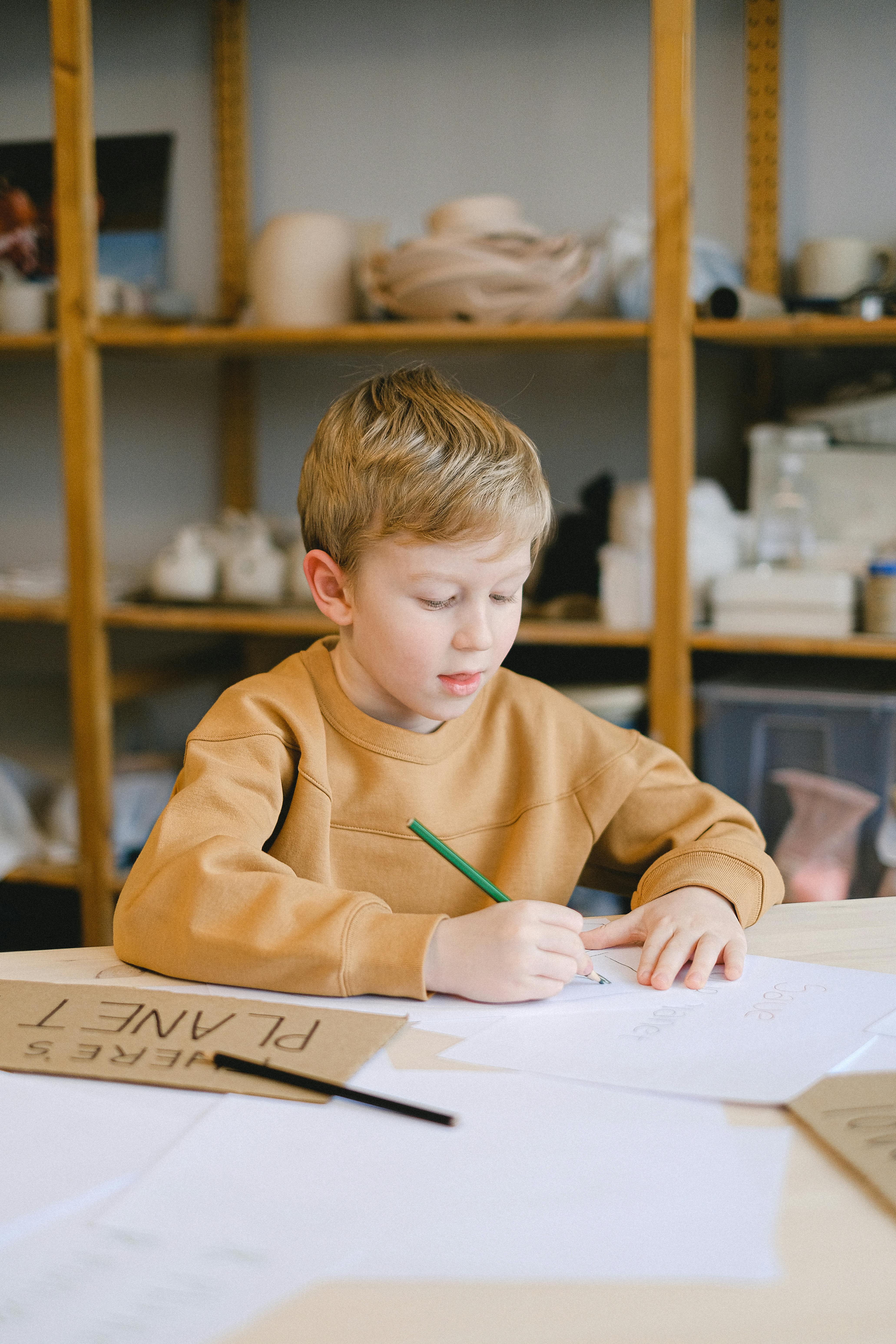 A Boy Writing with a Green Colored Pencil · Free Stock Photo