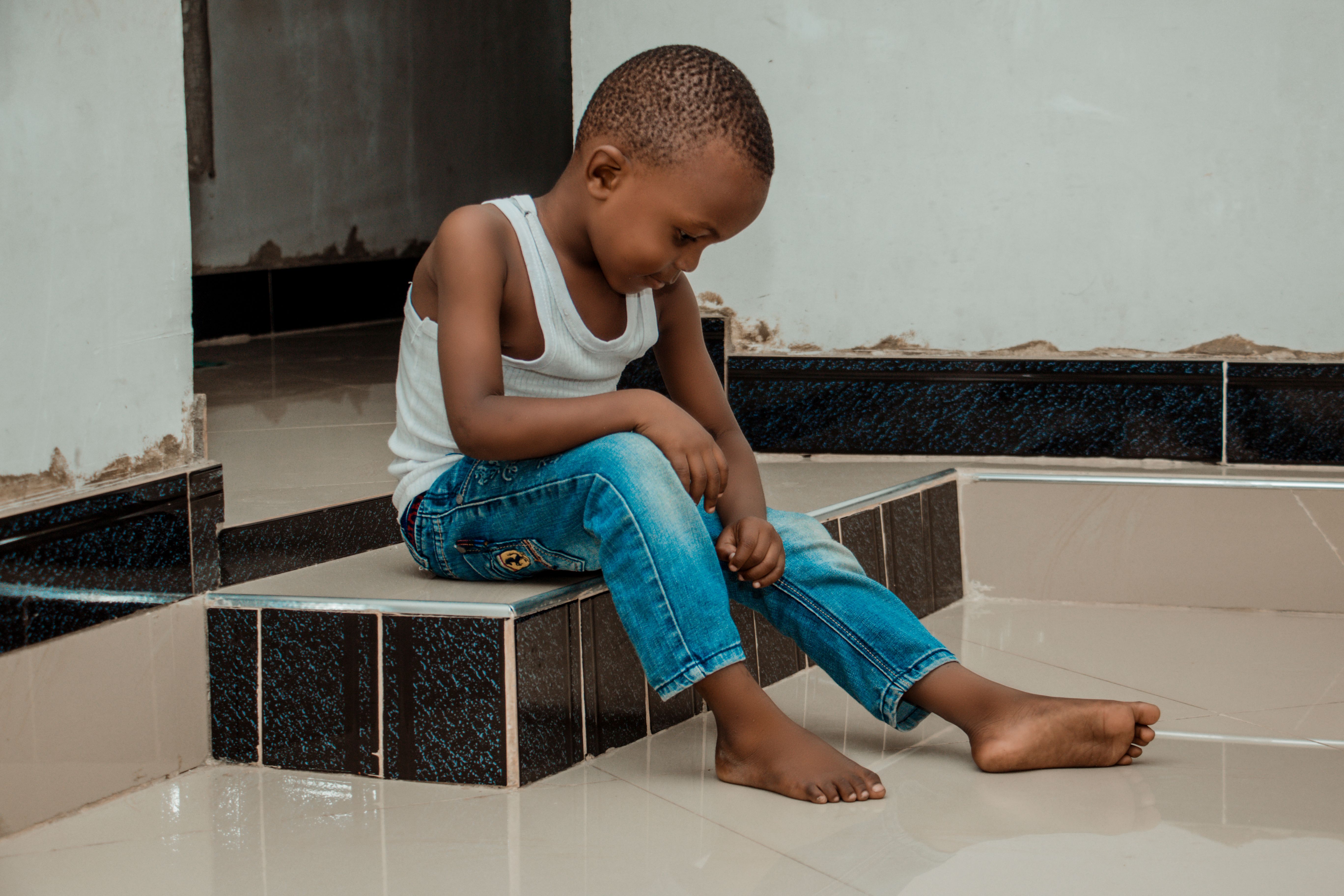 A Boy Sitting on the Floor while Looking at the Denim Pants He is ...