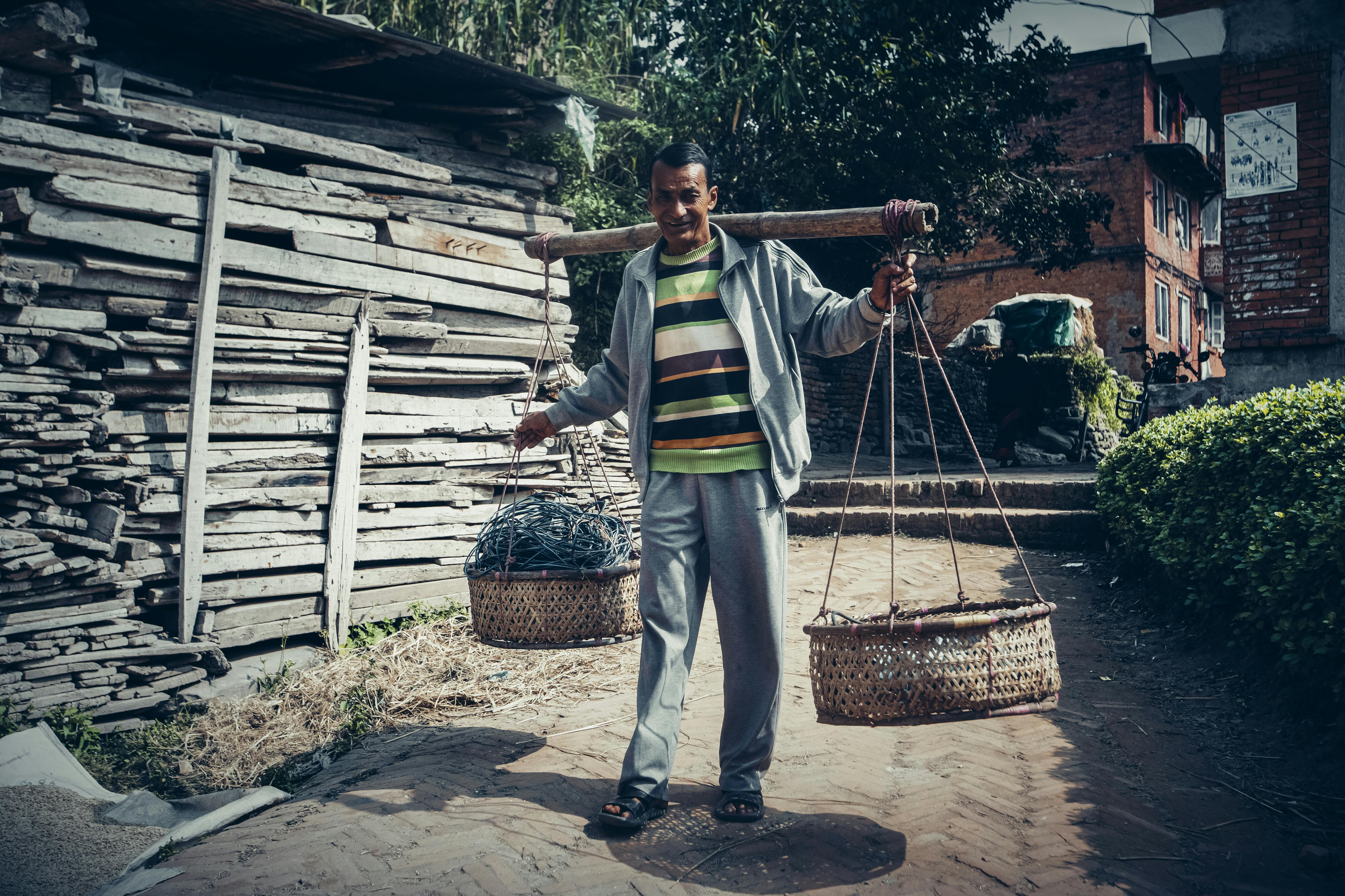A Man Carrying Baskets Balanced in a Bamboo Pole · Free Stock Photo