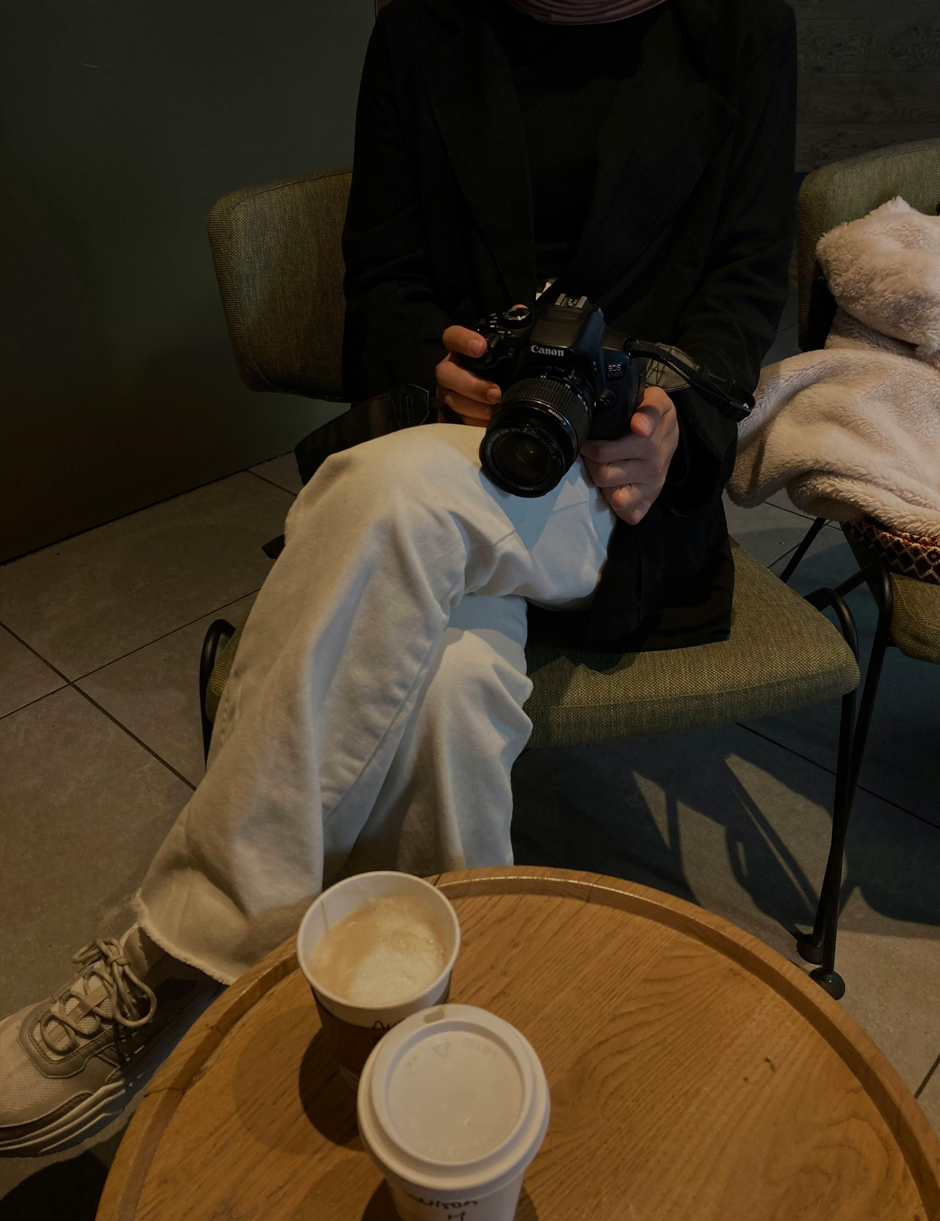 Photographer Sitting with a Camera by a Table with Two Disposable ...
