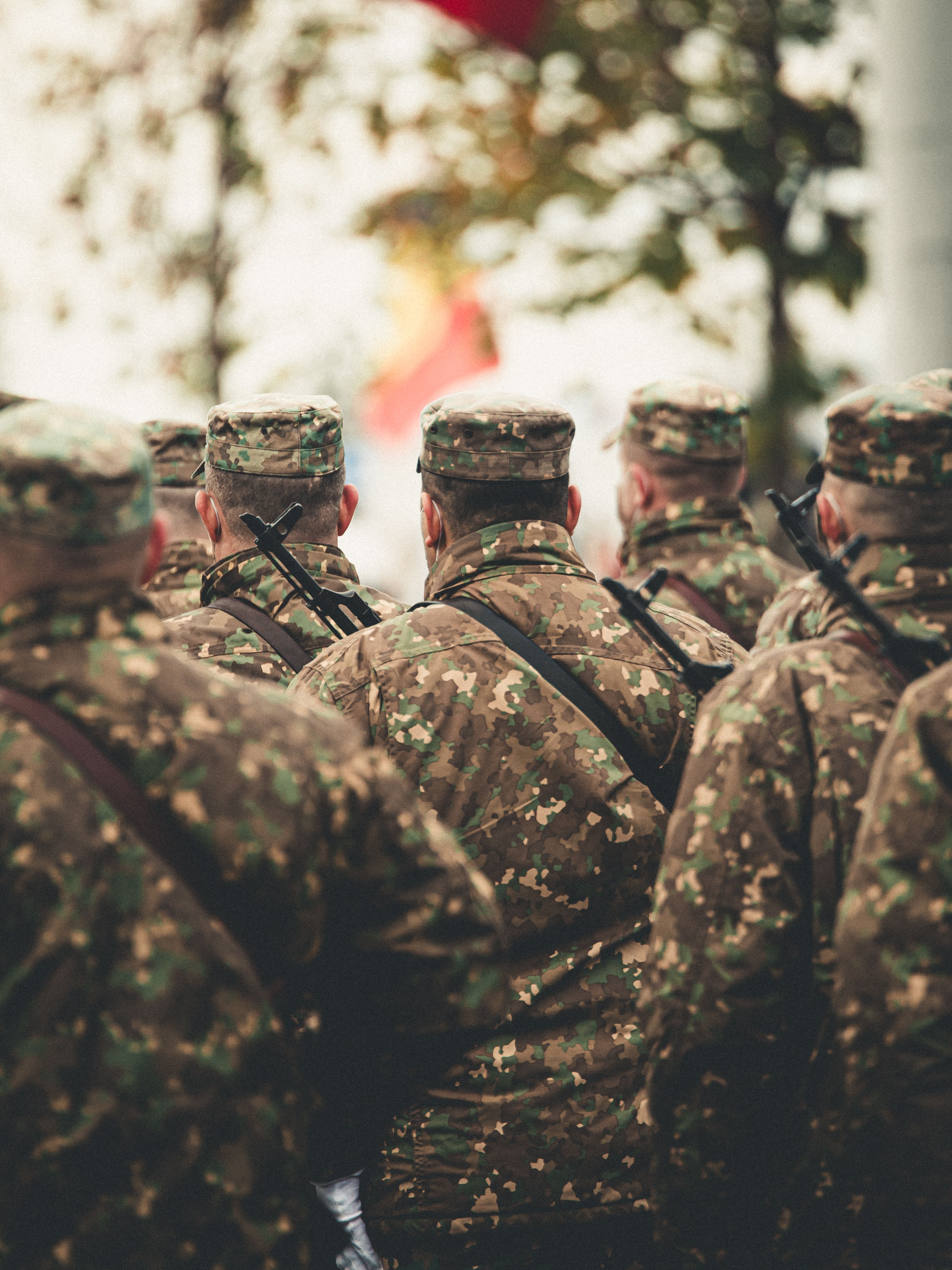 Armed Men Standing Near People Sitting in Line Near Camp · Free Stock Photo