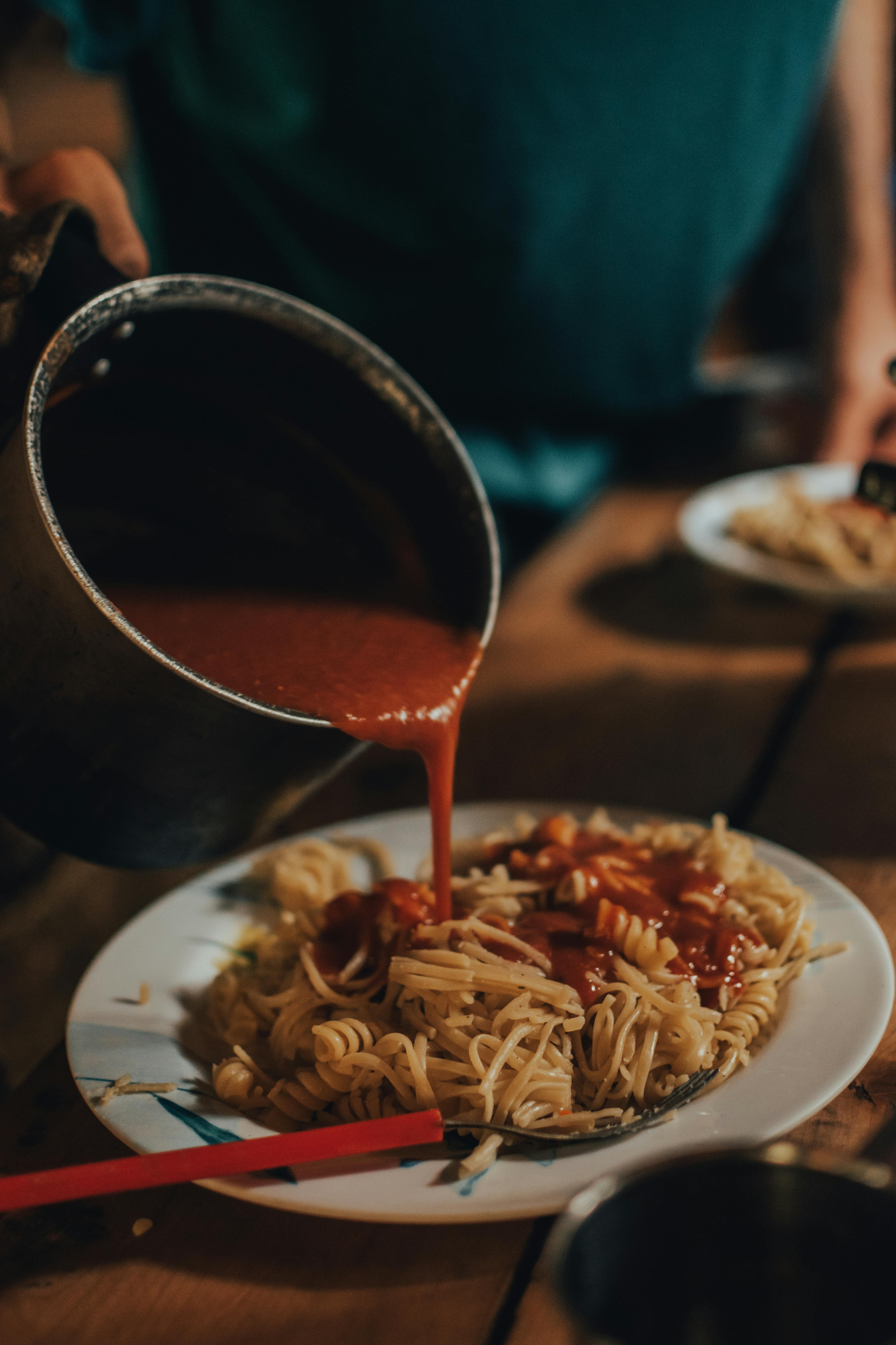 Poring Sauce over a Plate of Pasta · Free Stock Photo