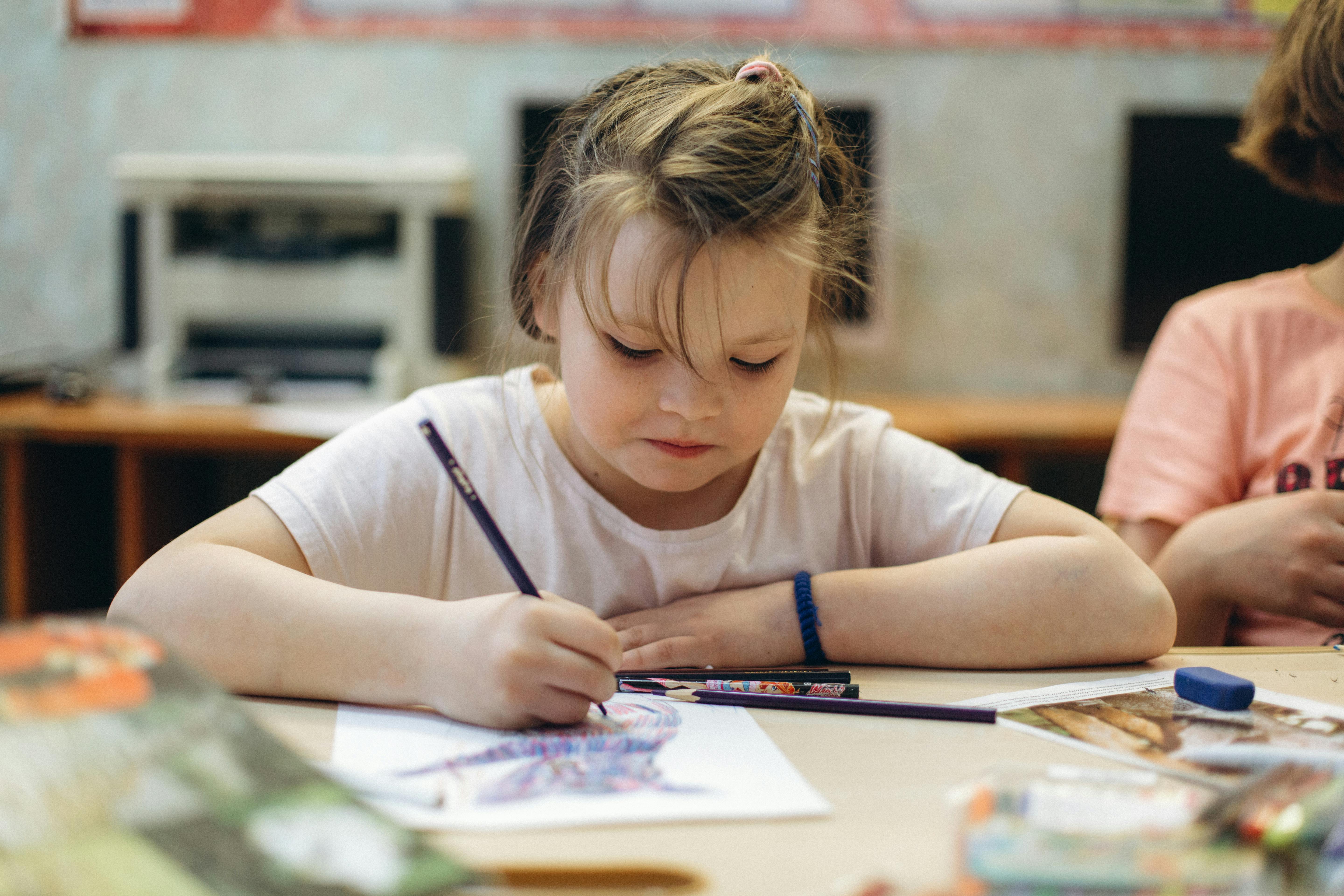 A Girl Coloring on White Paper Using a Color Pencil · Free Stock Photo