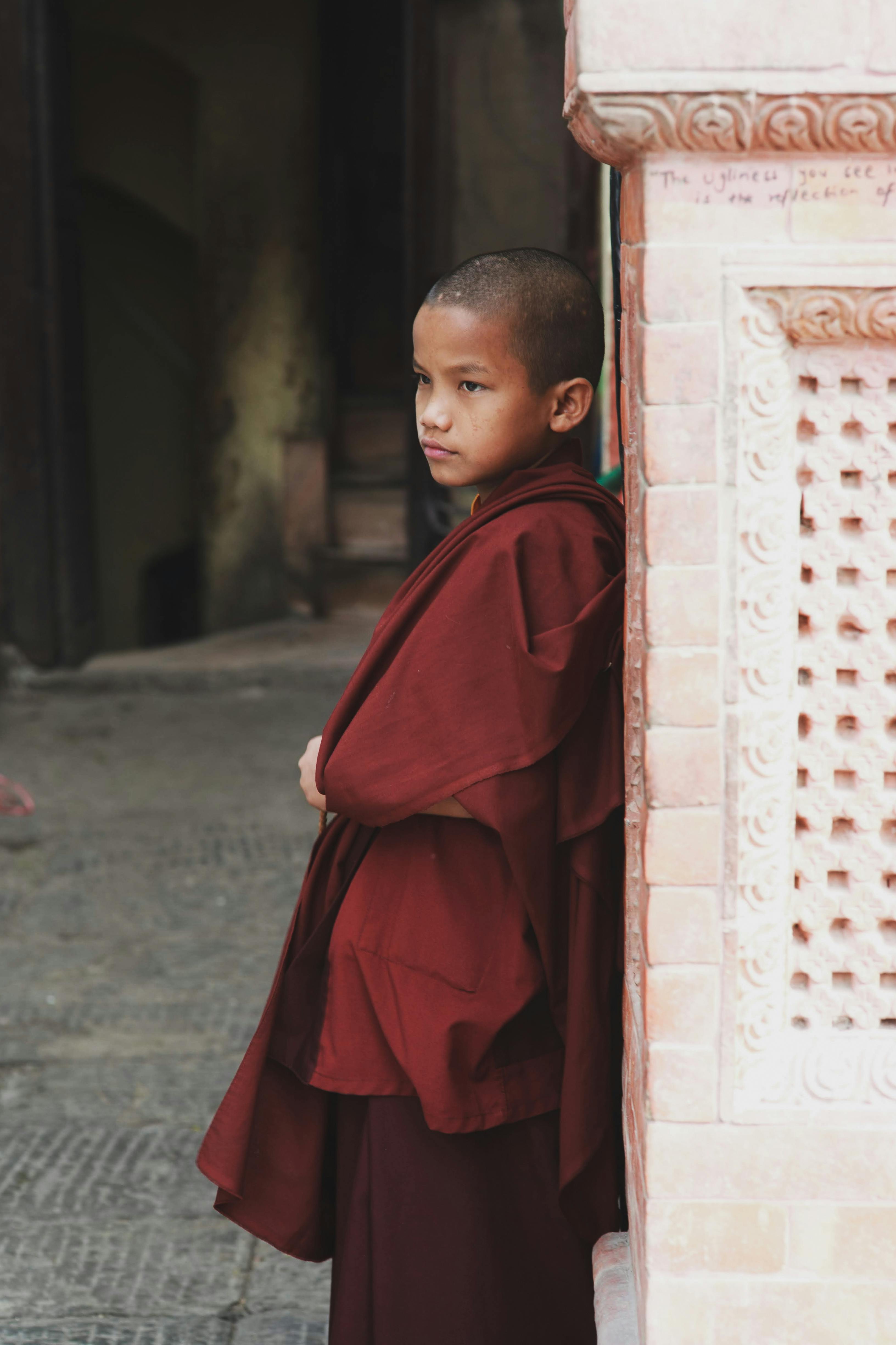 Little Boy in Monk Robes Leaning Against Pillar · Free Stock Photo