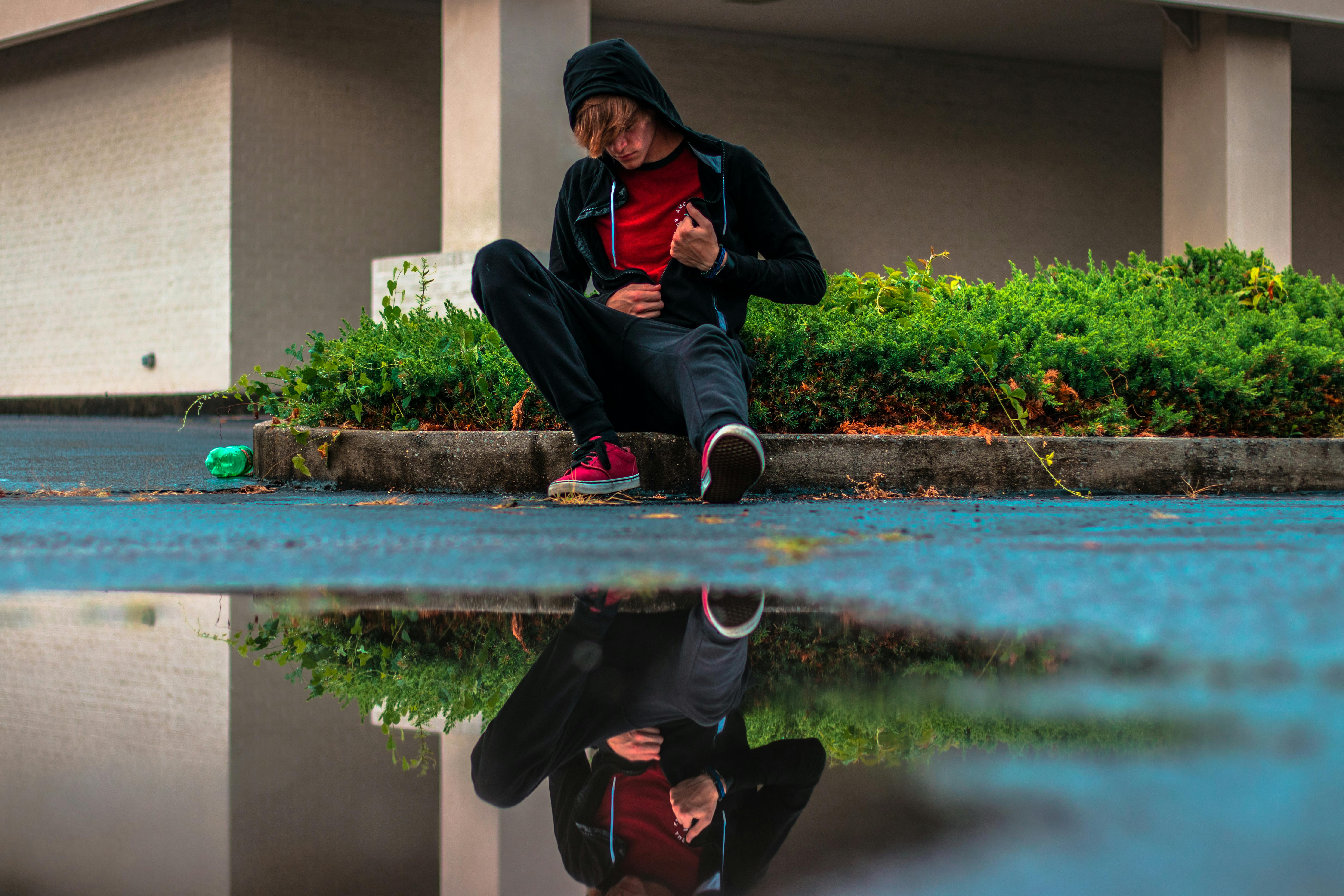 Boy Sitting on Gray Concrete Pavement · Free Stock Photo