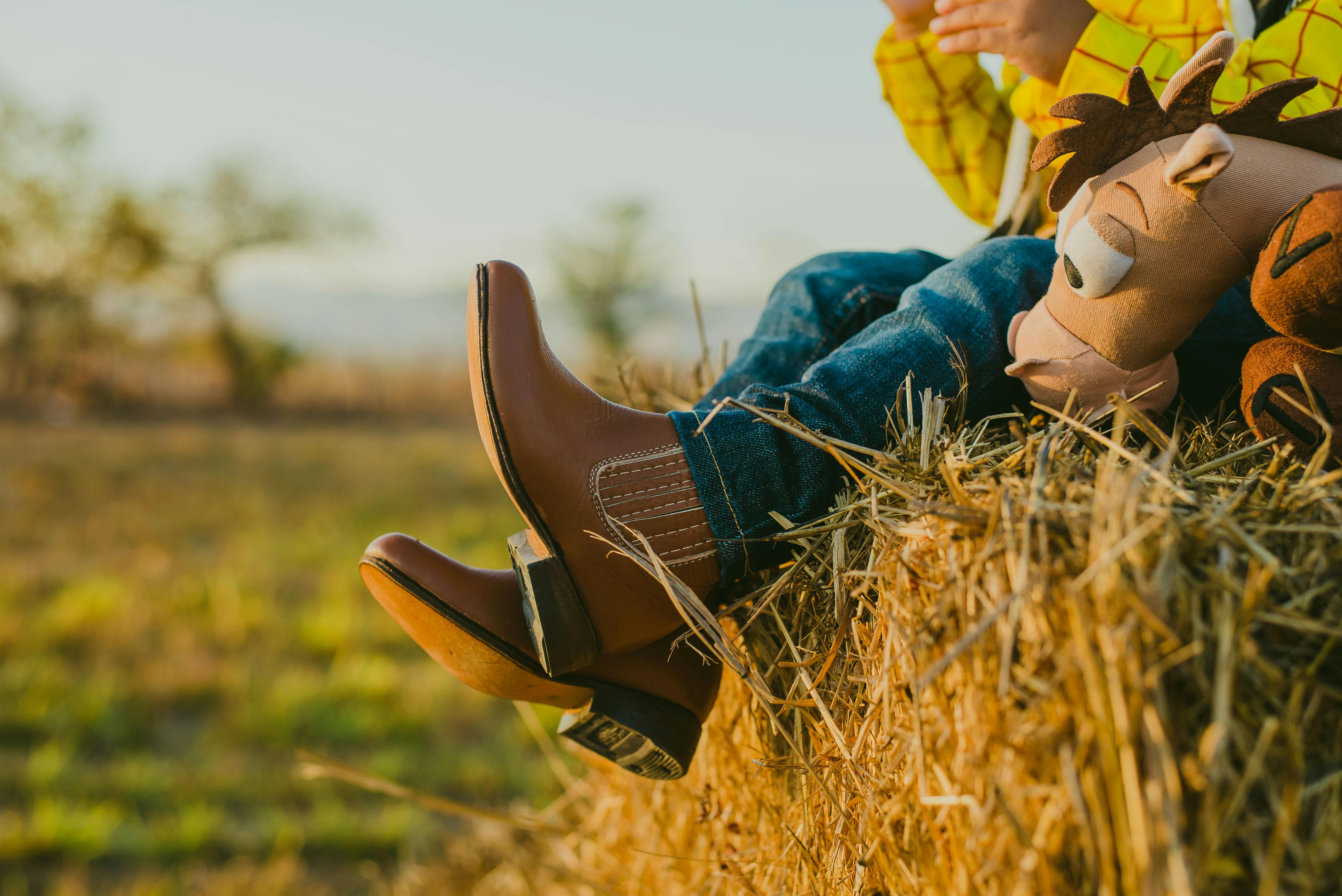 Close-Up Shot of a Kid in Boots Sitting on a Haystack · Free Stock Photo