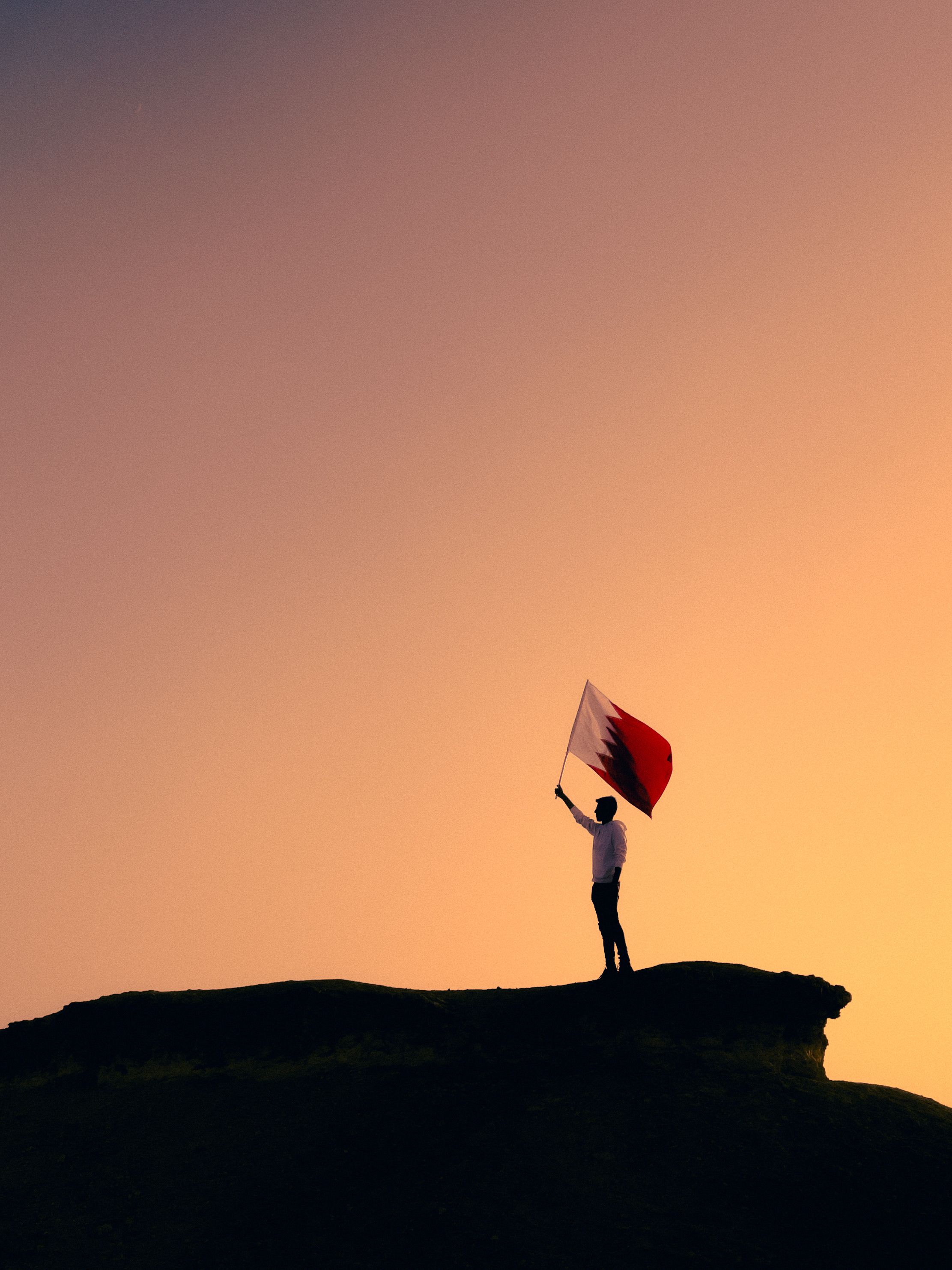A Person Standing on Top of a Cliff Holding a Red and White Flag · Free ...